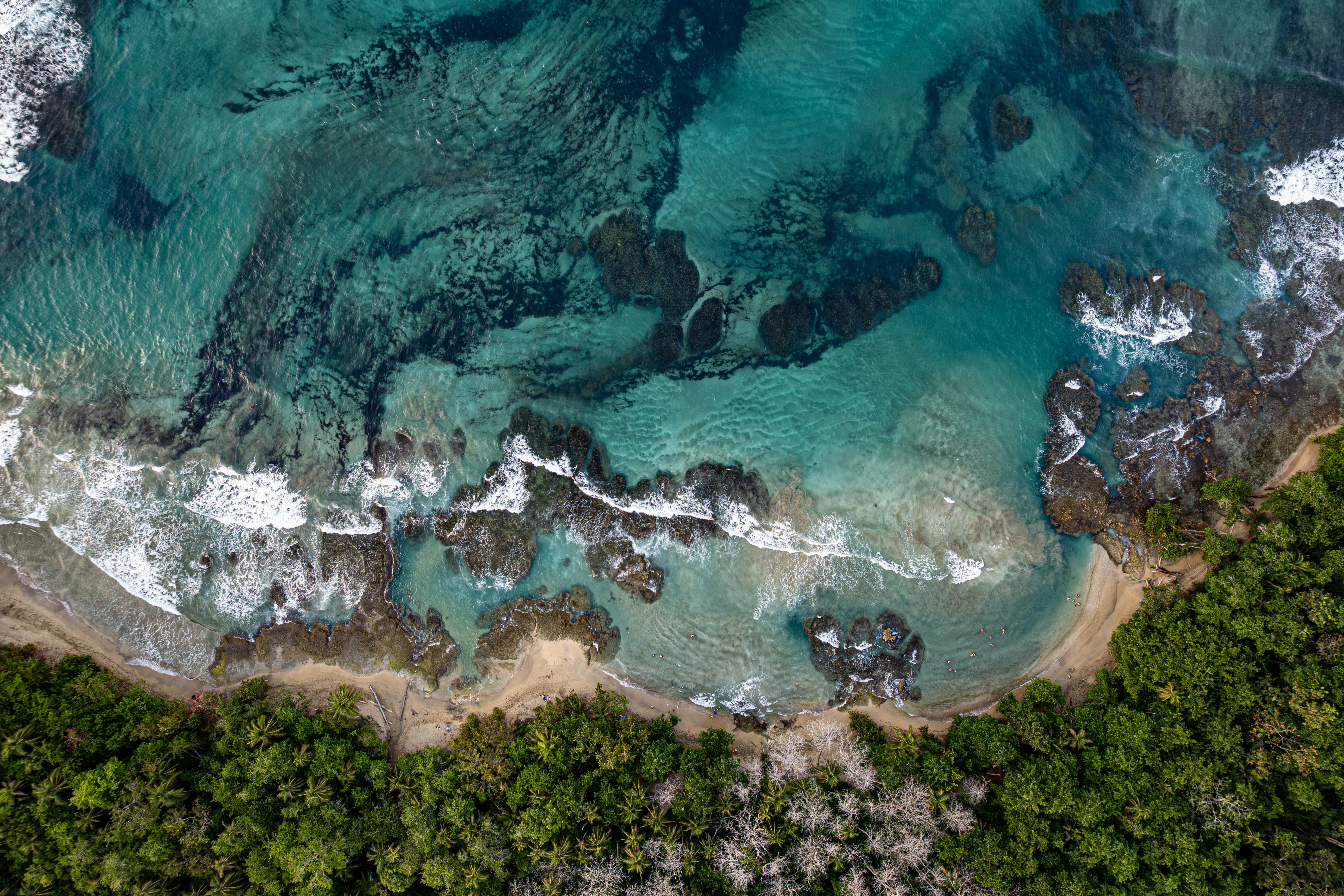 Emerald-green coastline with turquoise shallows meeting a sandy beach, bordered by dense jungle below.