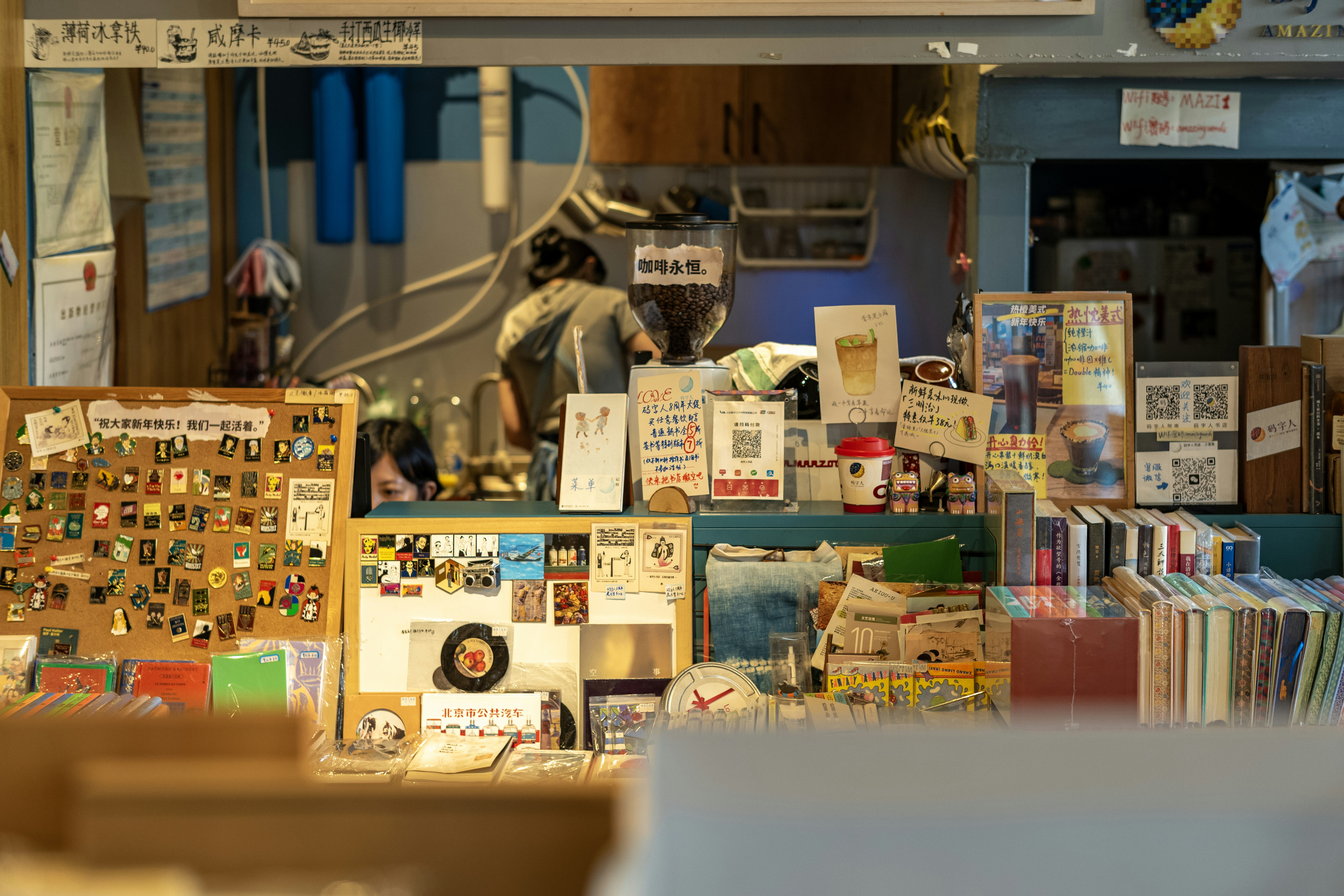 Vibrant display of books, postcards, and trinkets fills a cozy shop counter, with a blurred background suggesting activity inside the store.