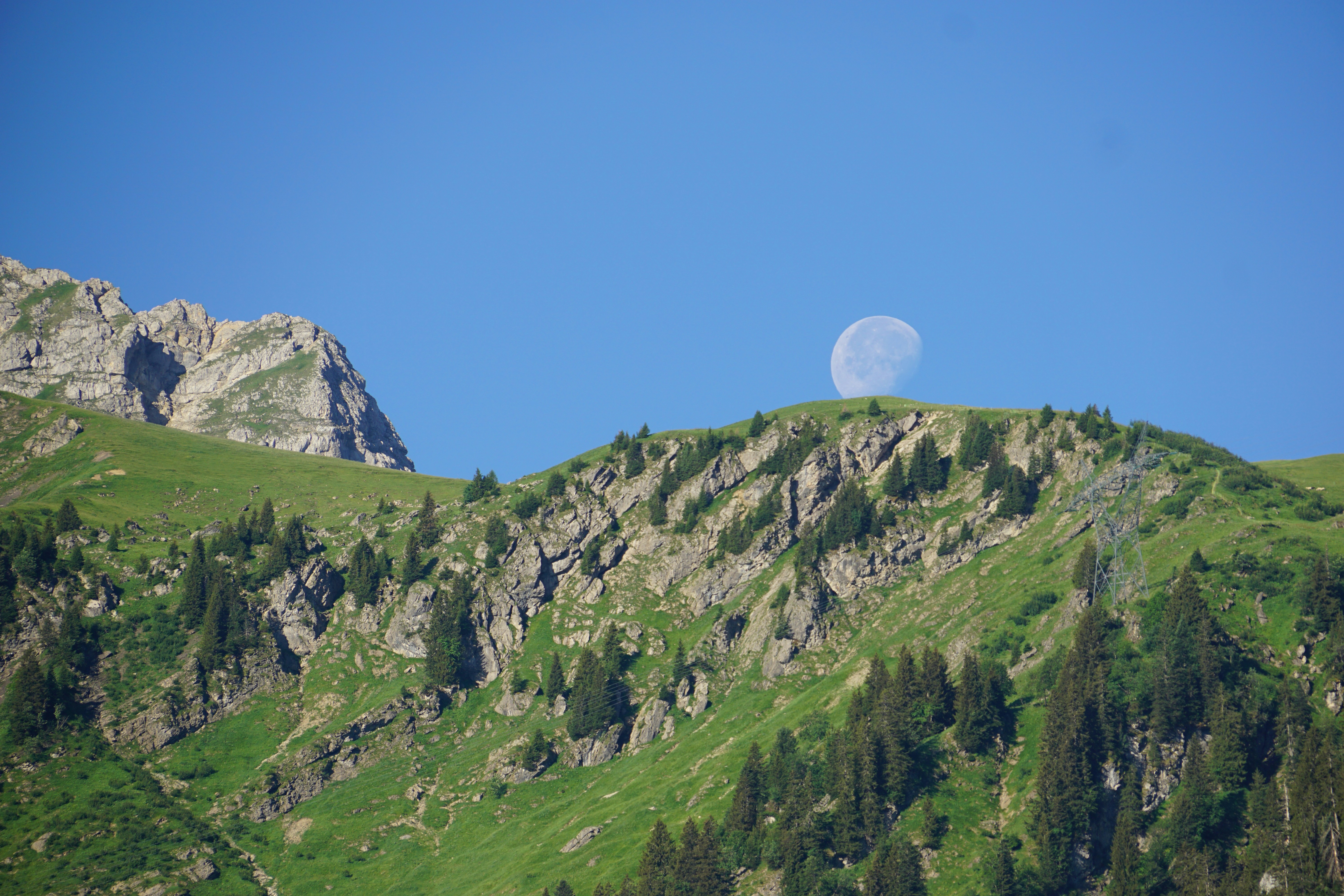 Moonlit Peak: The Moon Rests on a Mountain Crest Under Clear Blue Sky