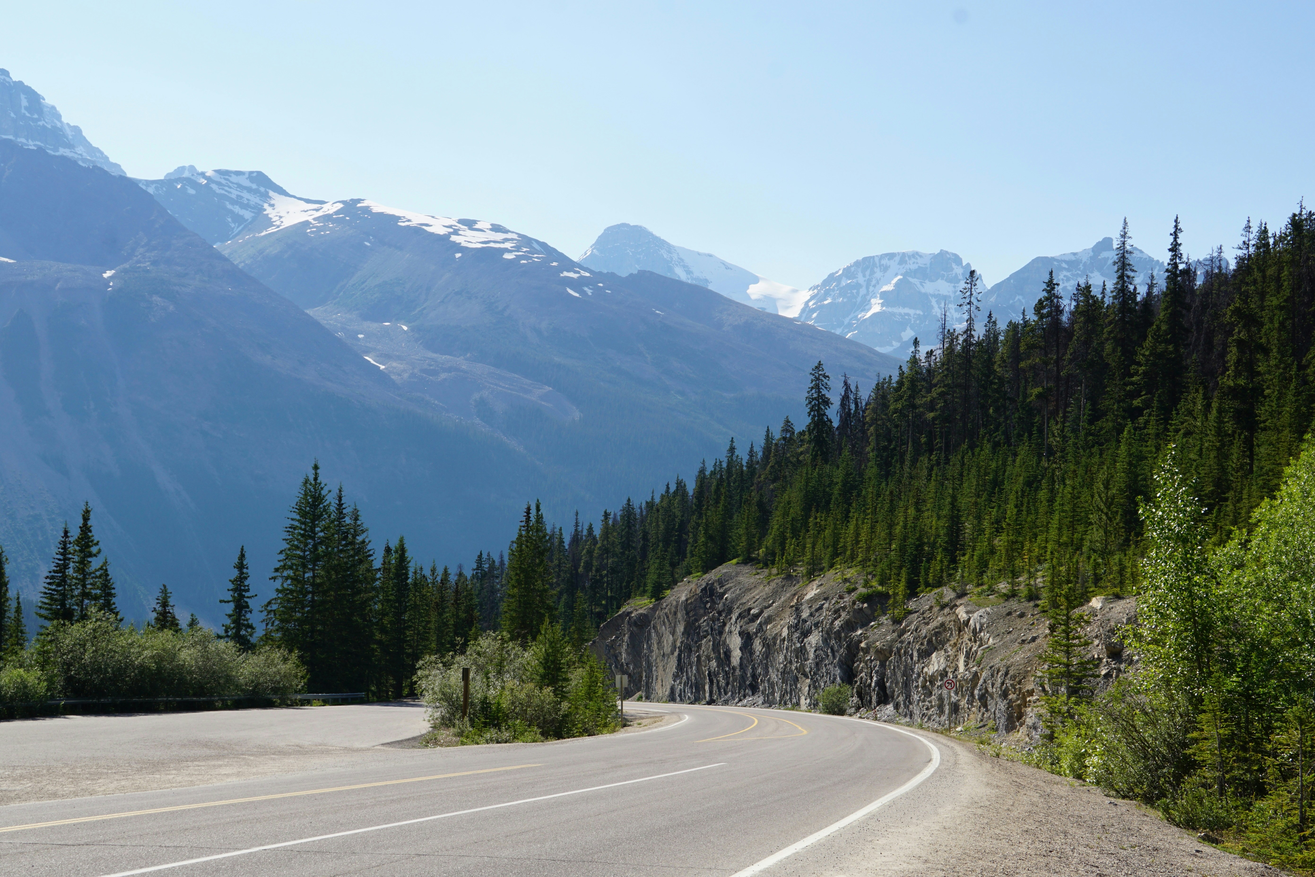 Paved mountain road curves through a forested valley toward distant snow‑fed peaks; the scene emphasizes depth and natural scenery. (photograph) 