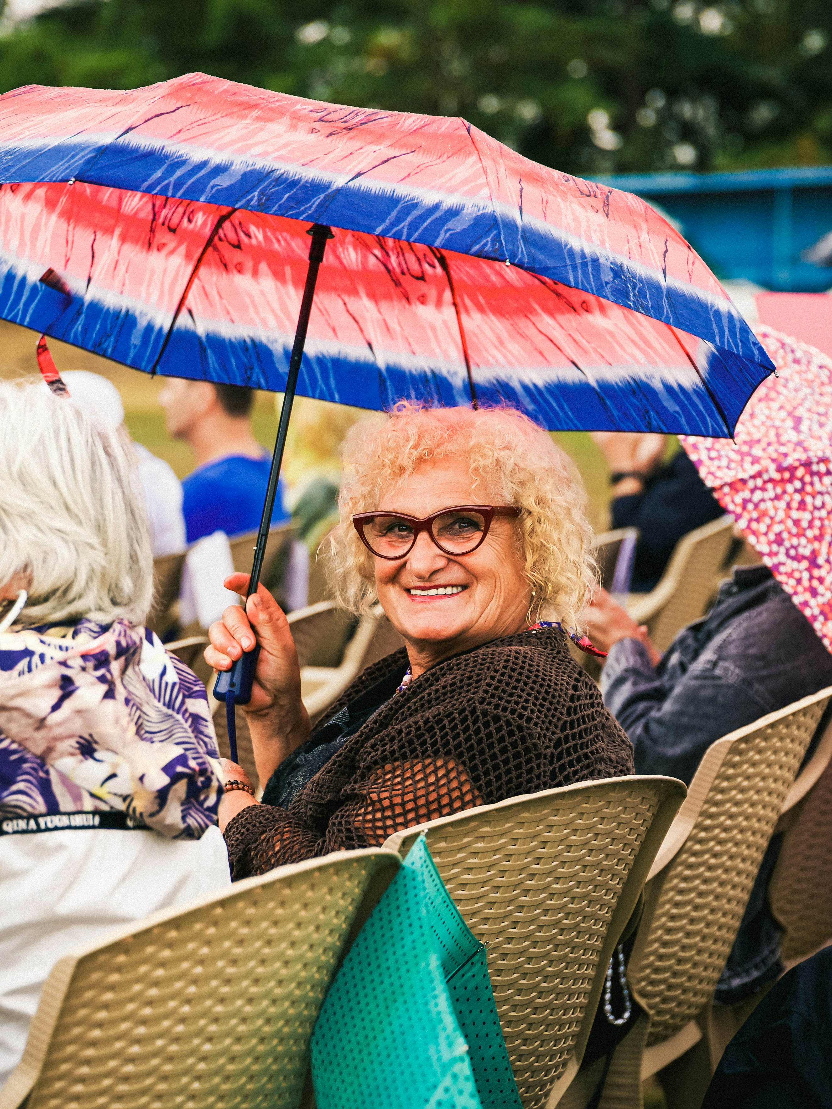 Smiling Vendor of Shade: A Senior Woman Under a Red-Blue Parasol