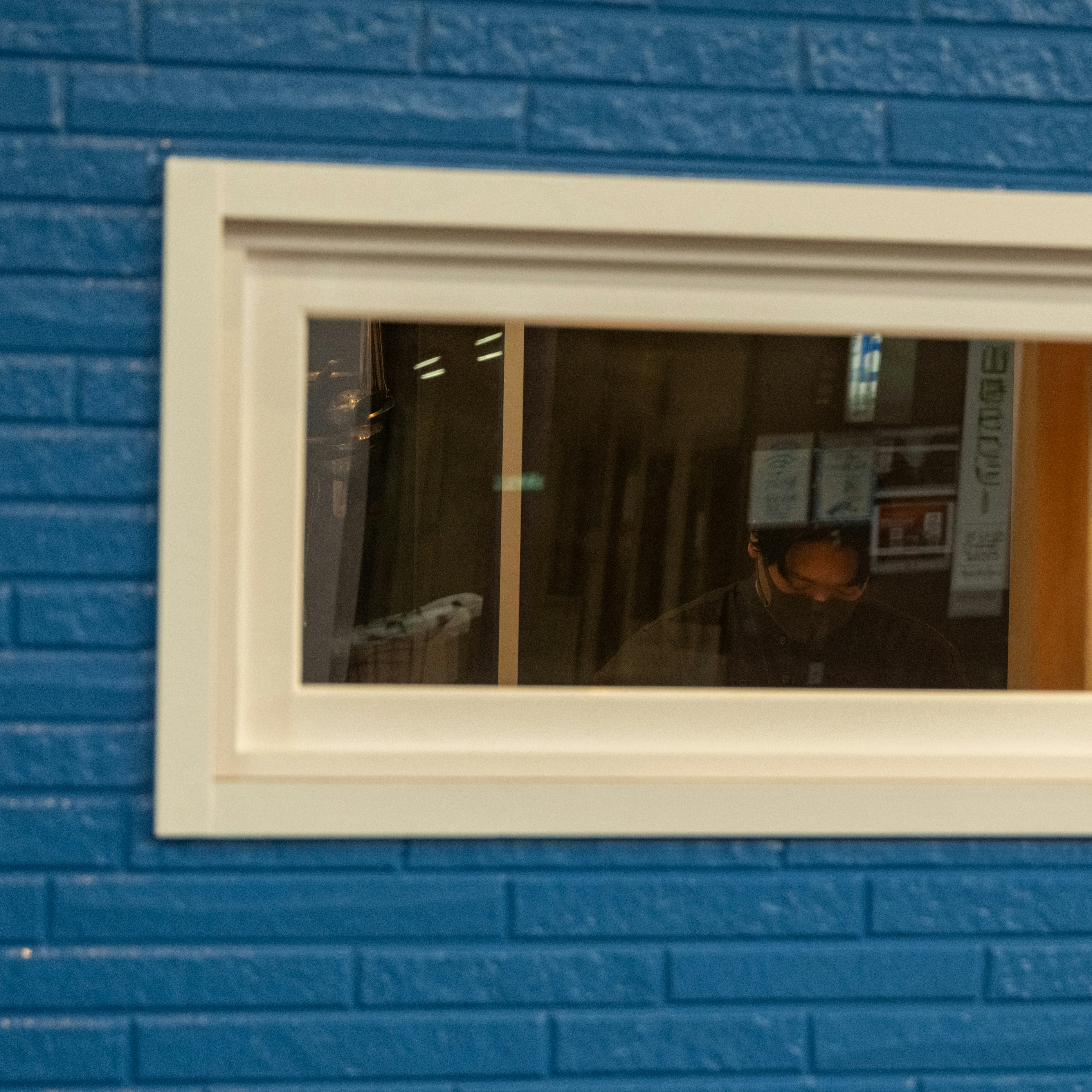 Windowed Quiet: A Masked Figure Reflected in Blue Brick