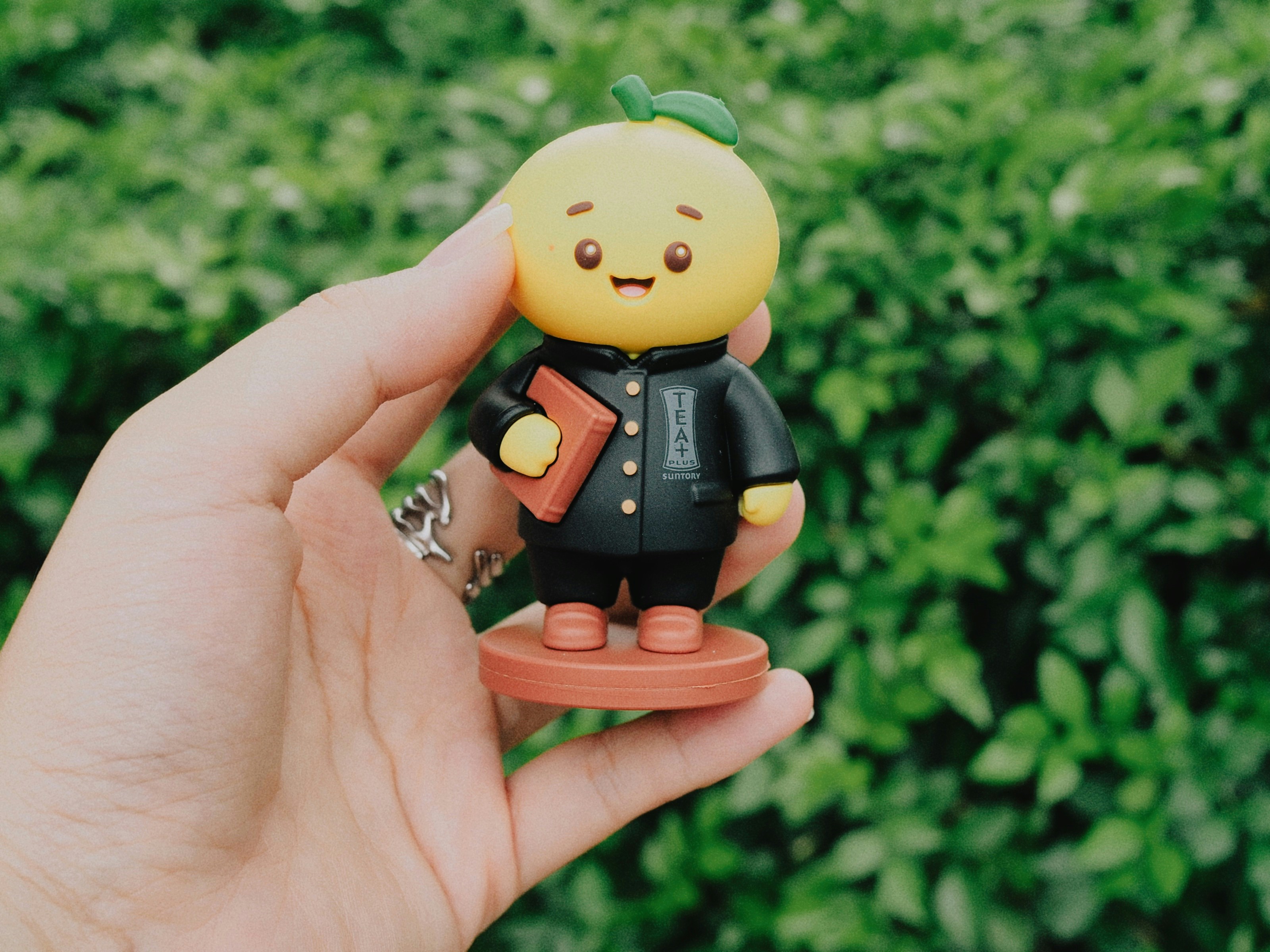 Happy yellow figurine in a tailored suit holds a tiny book against a leafy backdrop