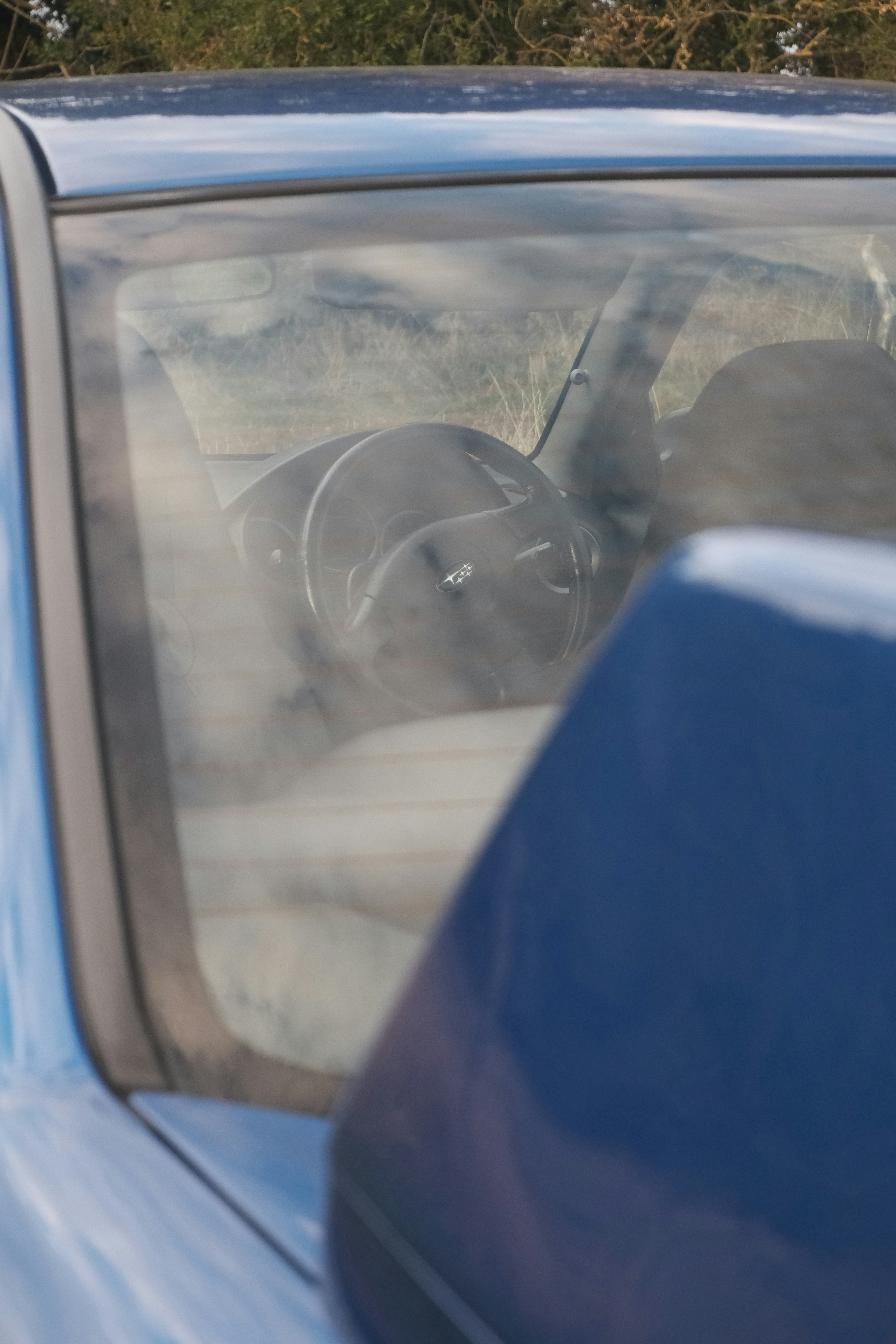 Softly blurred interior view through a car window, emphasizing the steering wheel and faint dashboard reflections inside a blue vehicle.