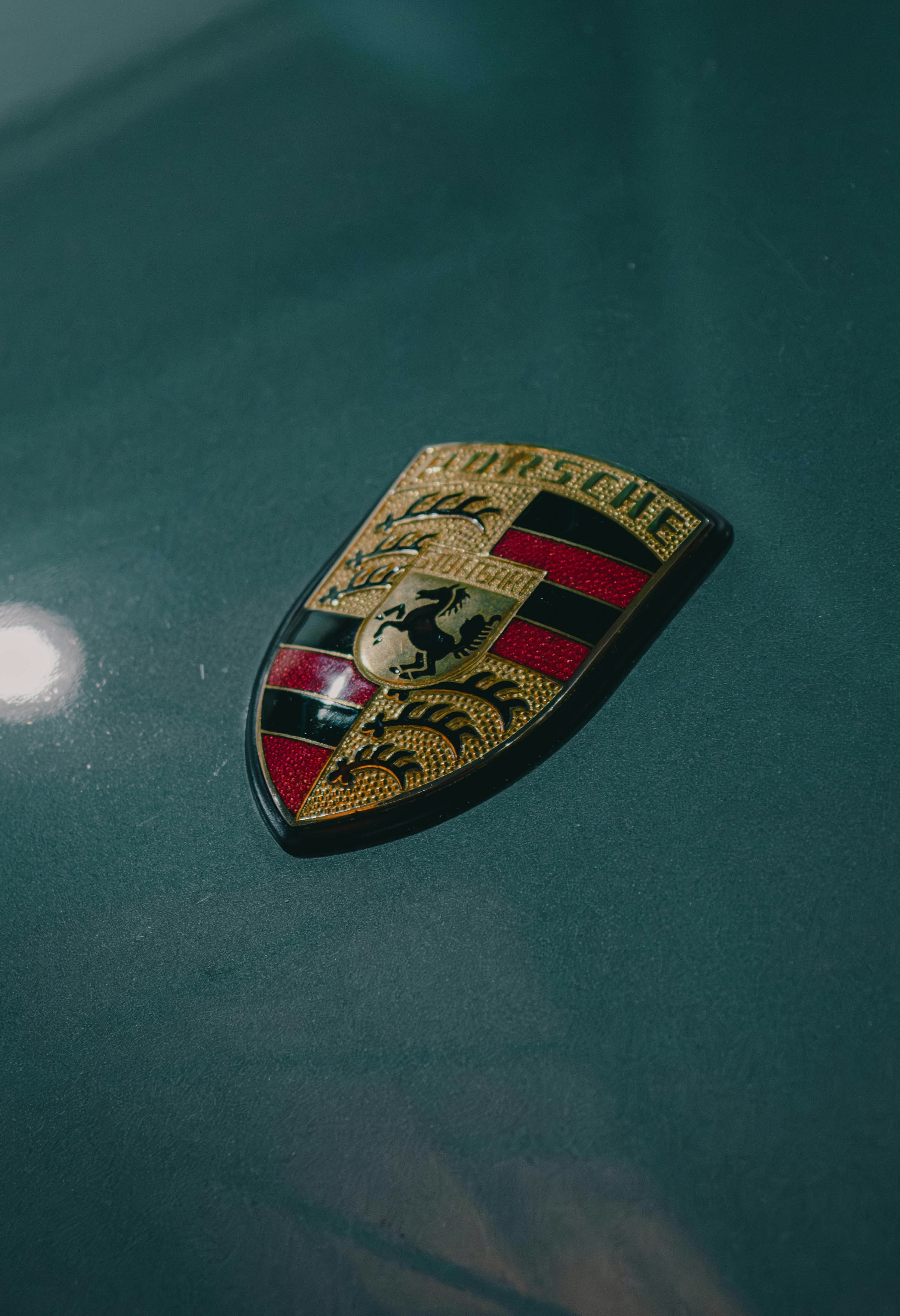 Emblem on Teal Canvas: Classic Porsche Crest Resting on Car Surface