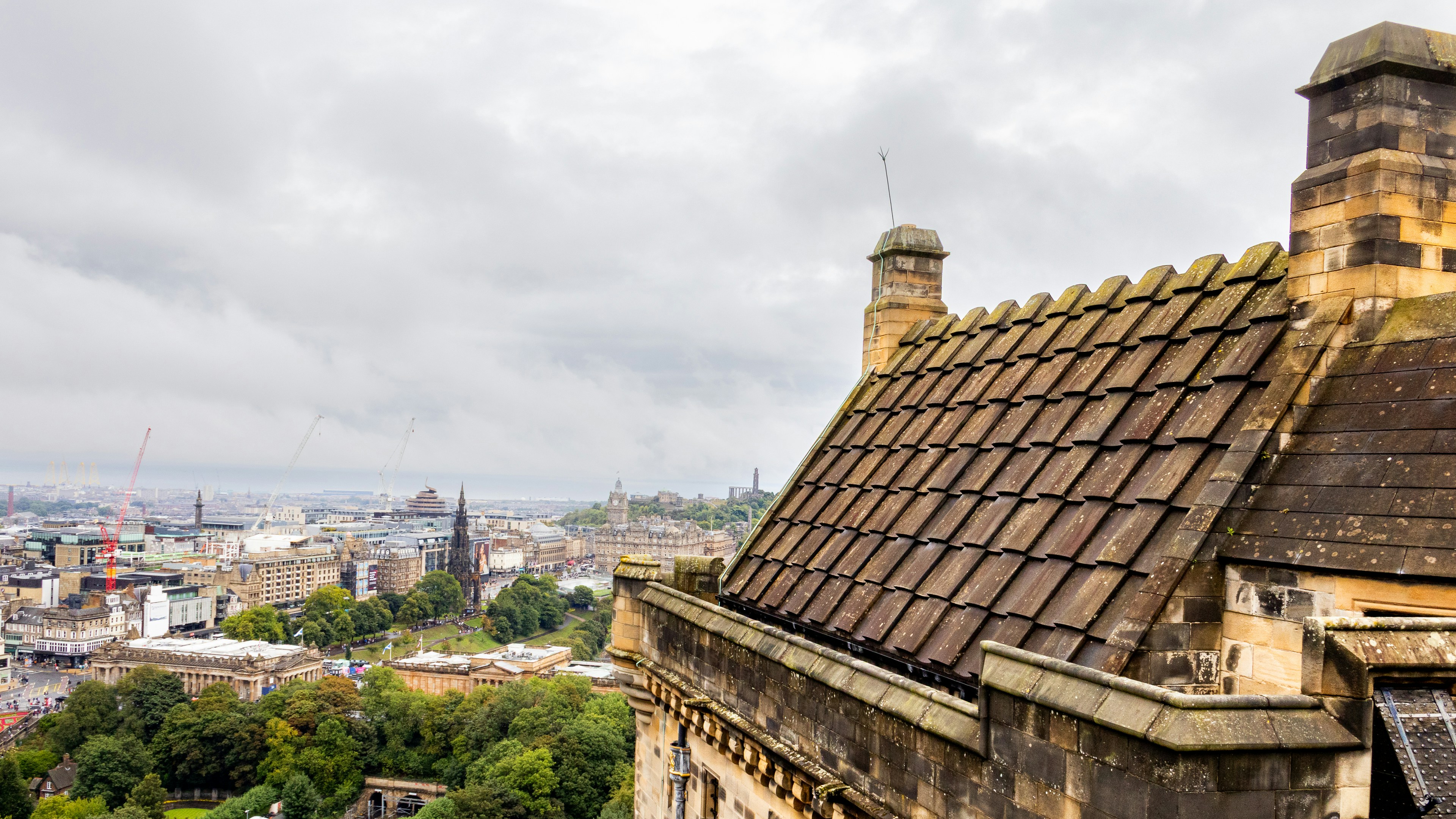 Cityscape view from a stone-tiled rooftop with distant skyline and green patches, capturing architectural details and overcast sky.