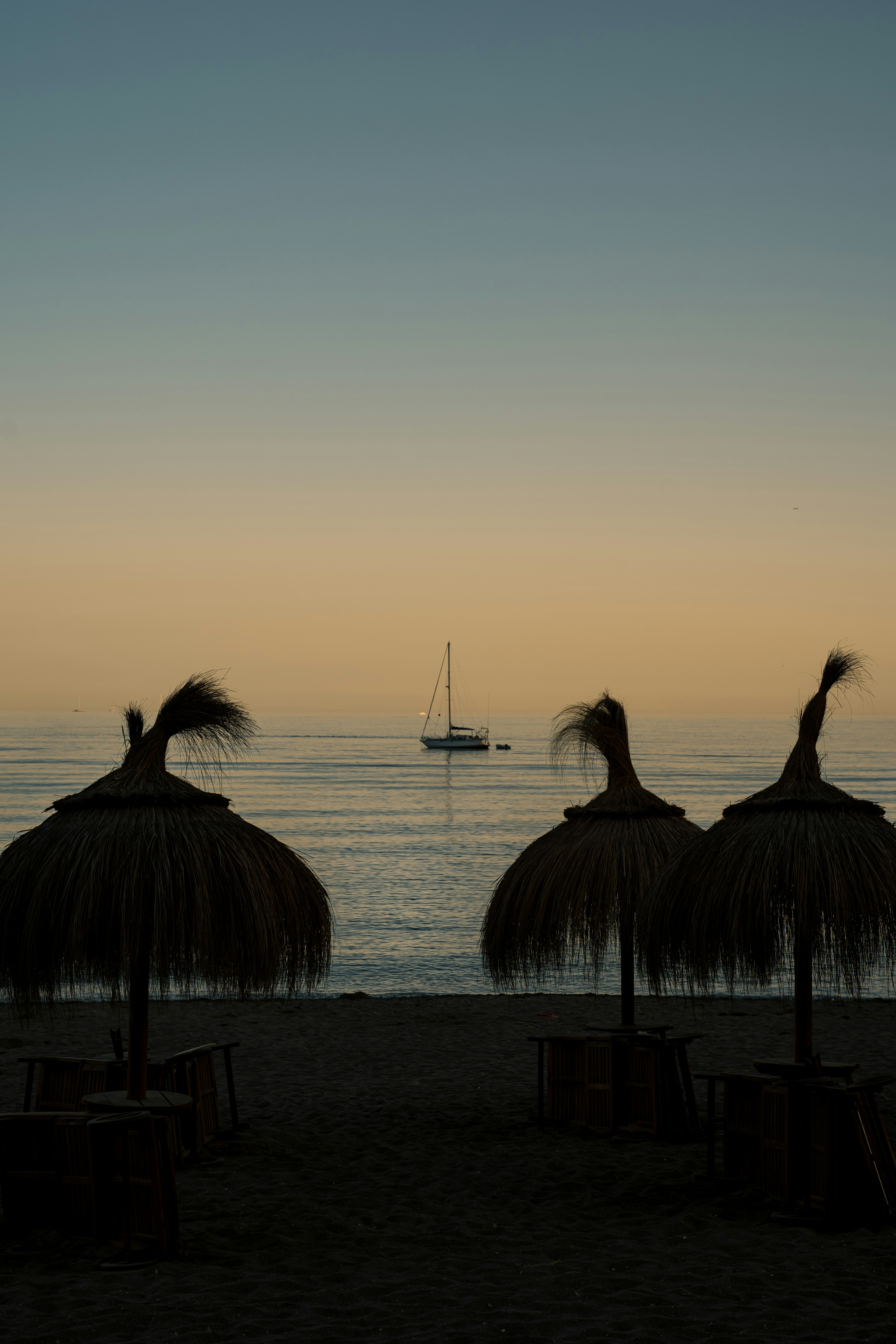 Silhouette at Sea: Dusk over the Beach with a Sloop on Calm Waters