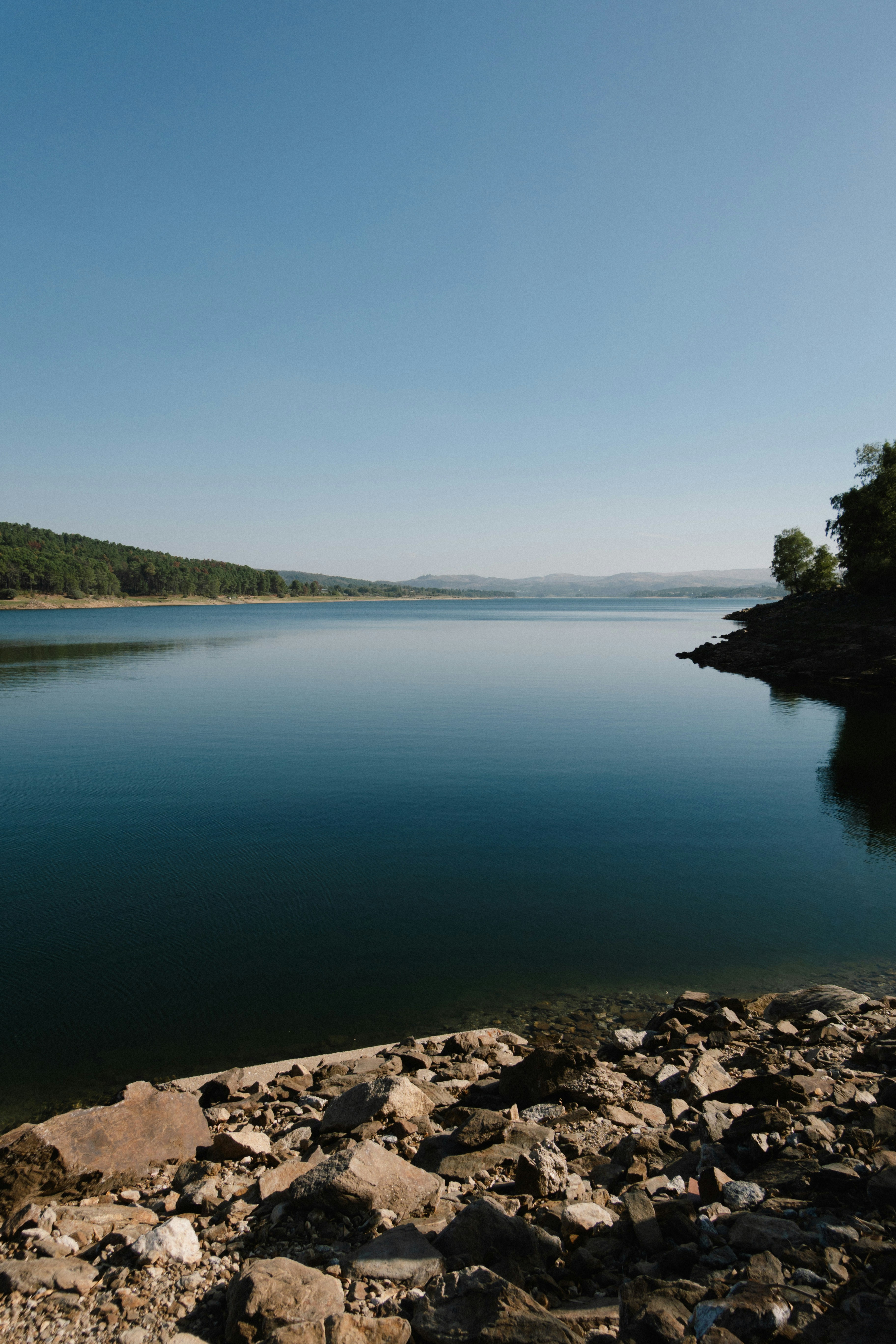 Quiet Reservoir Edge: Stones, Water, and Distant Hills