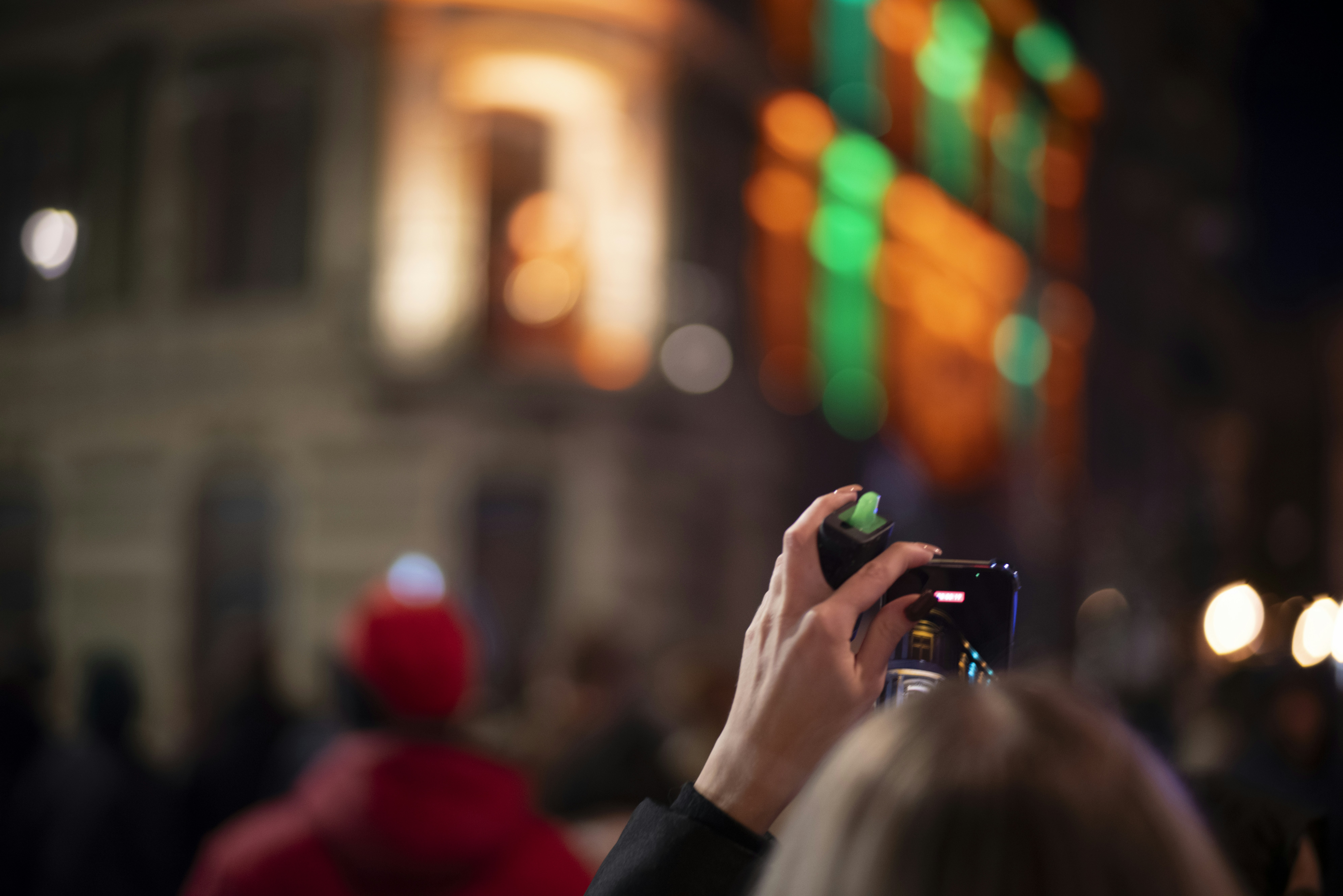 Blurred nightlife street scene with a raised camera in the foreground and colorful lights in the background.