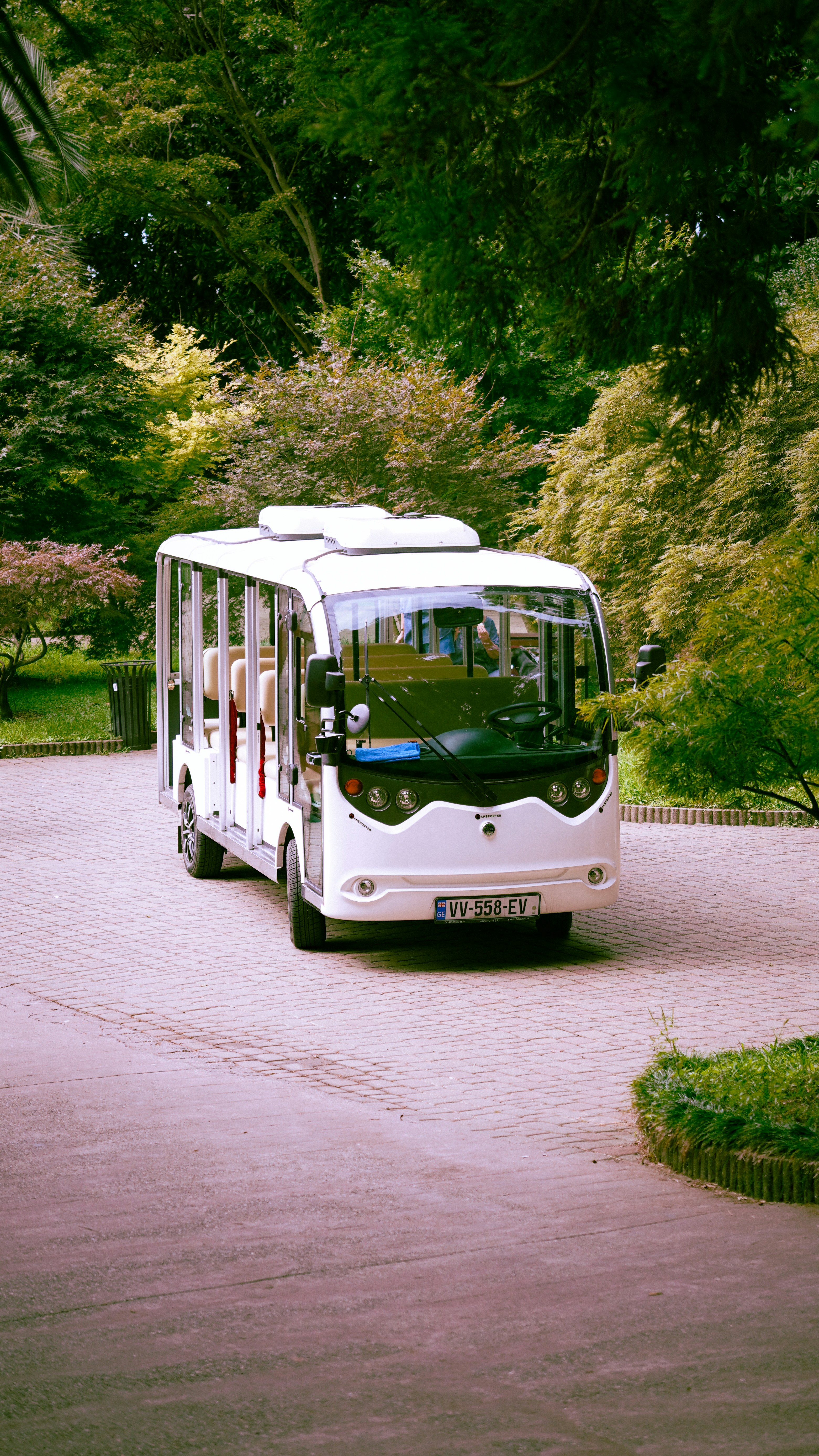 White shuttle through a green park A quiet tour vehicle on a cobblestone path