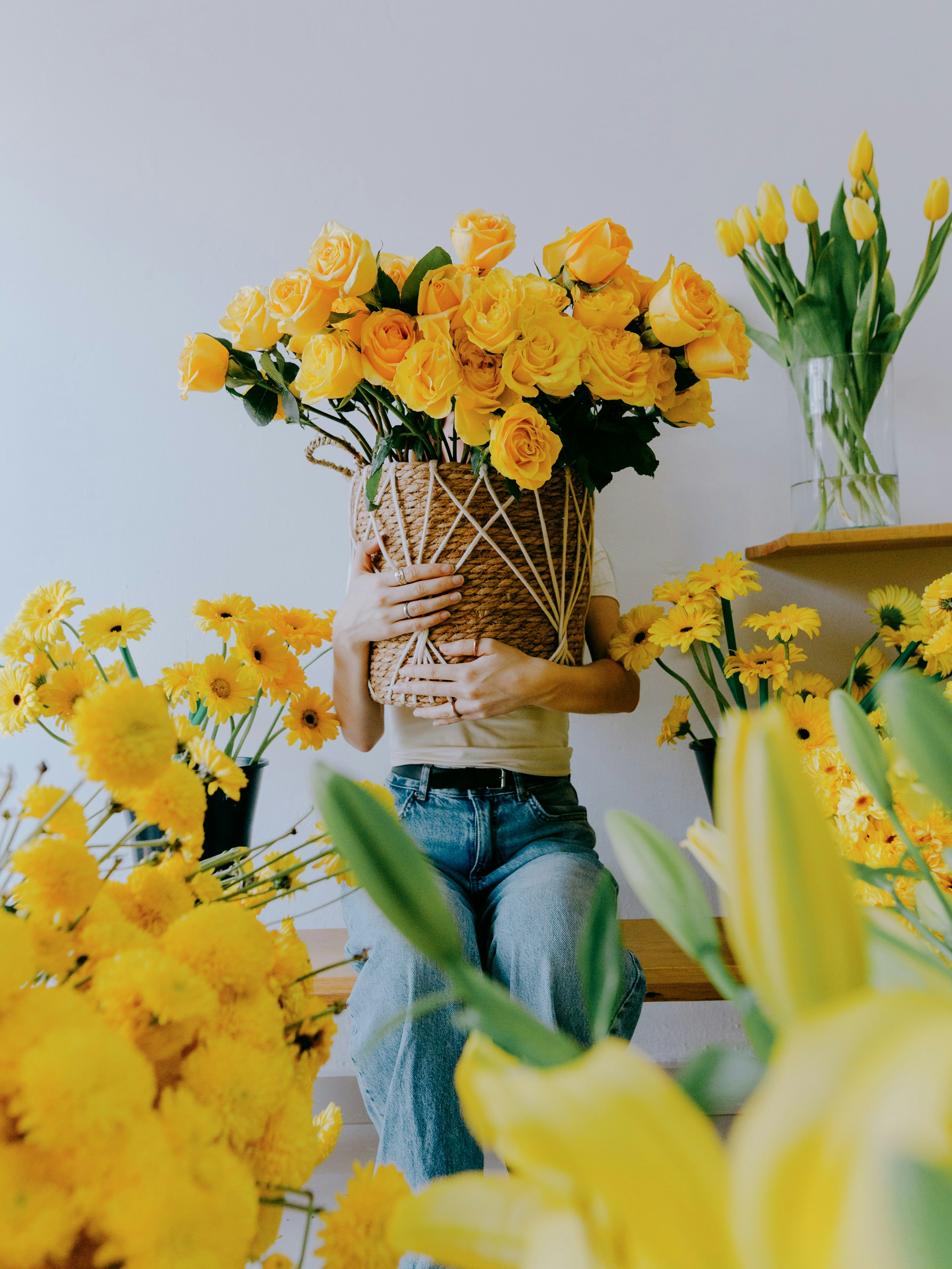 A person holding a large basket of yellow roses surrounded by yellow flowers