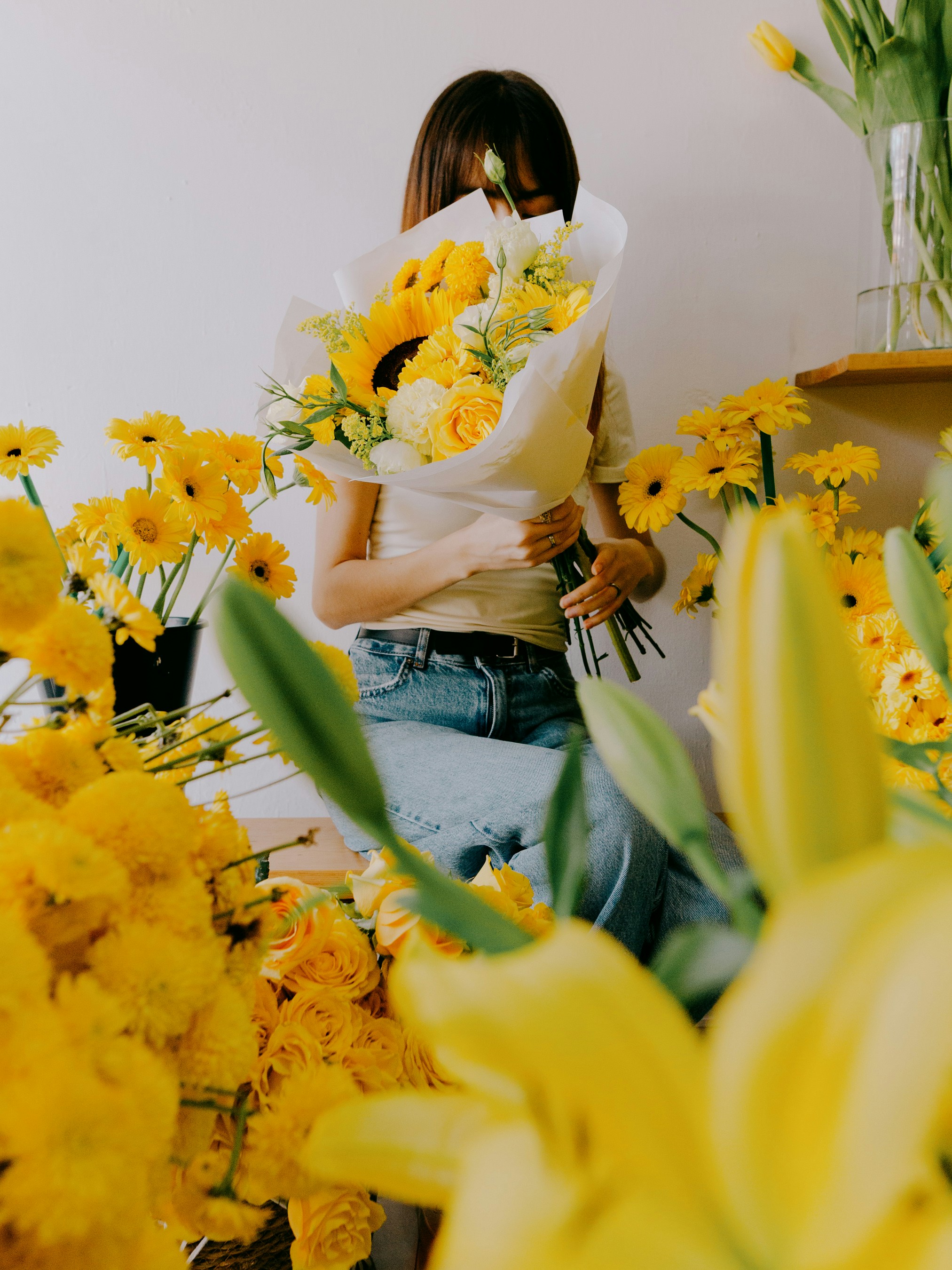 A person holding a large bouquet of yellow sunflowers and roses in a flower shop