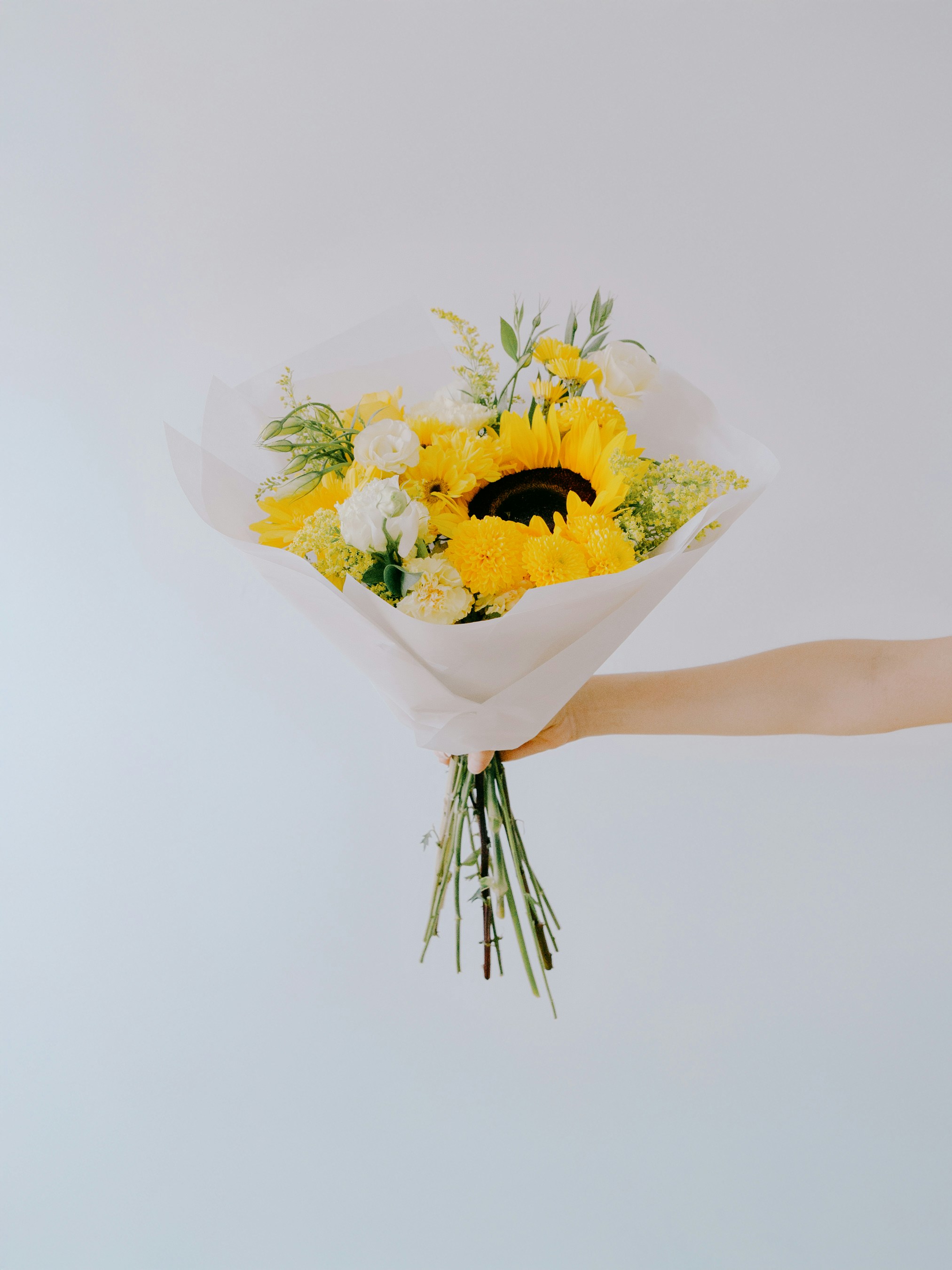 Bright bouquet of sunflowers and white blooms pinched by a pale arm against a soft backdrop