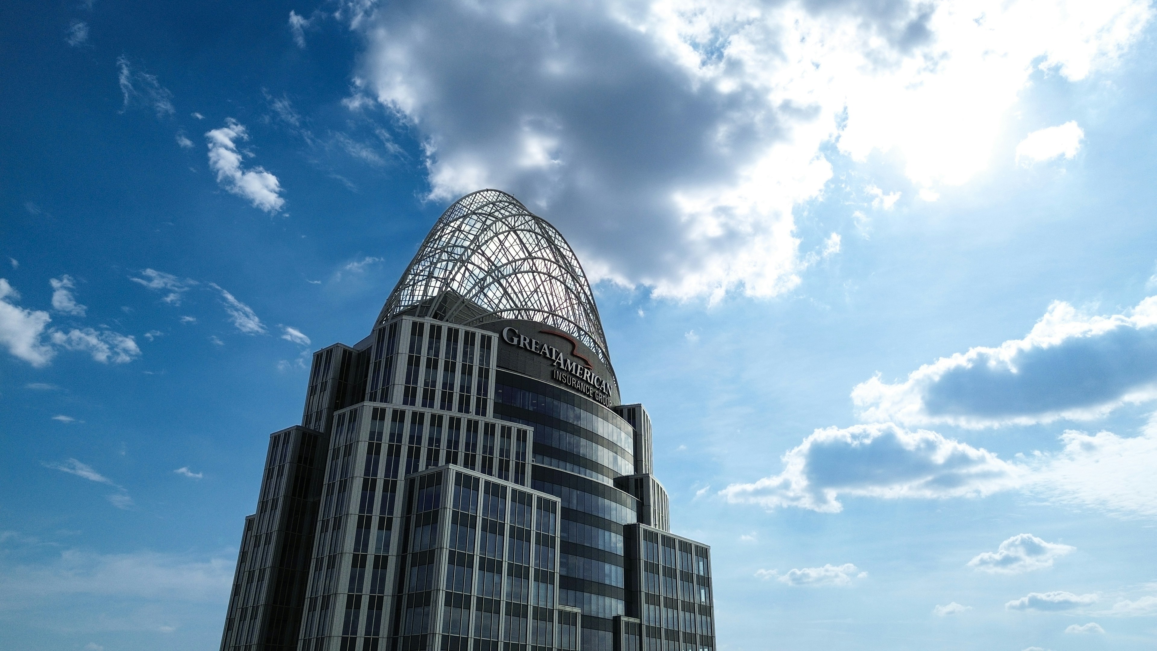 Architectural centerpiece with a glass dome rises above a modern glass-clad tower, set against a bright sky.