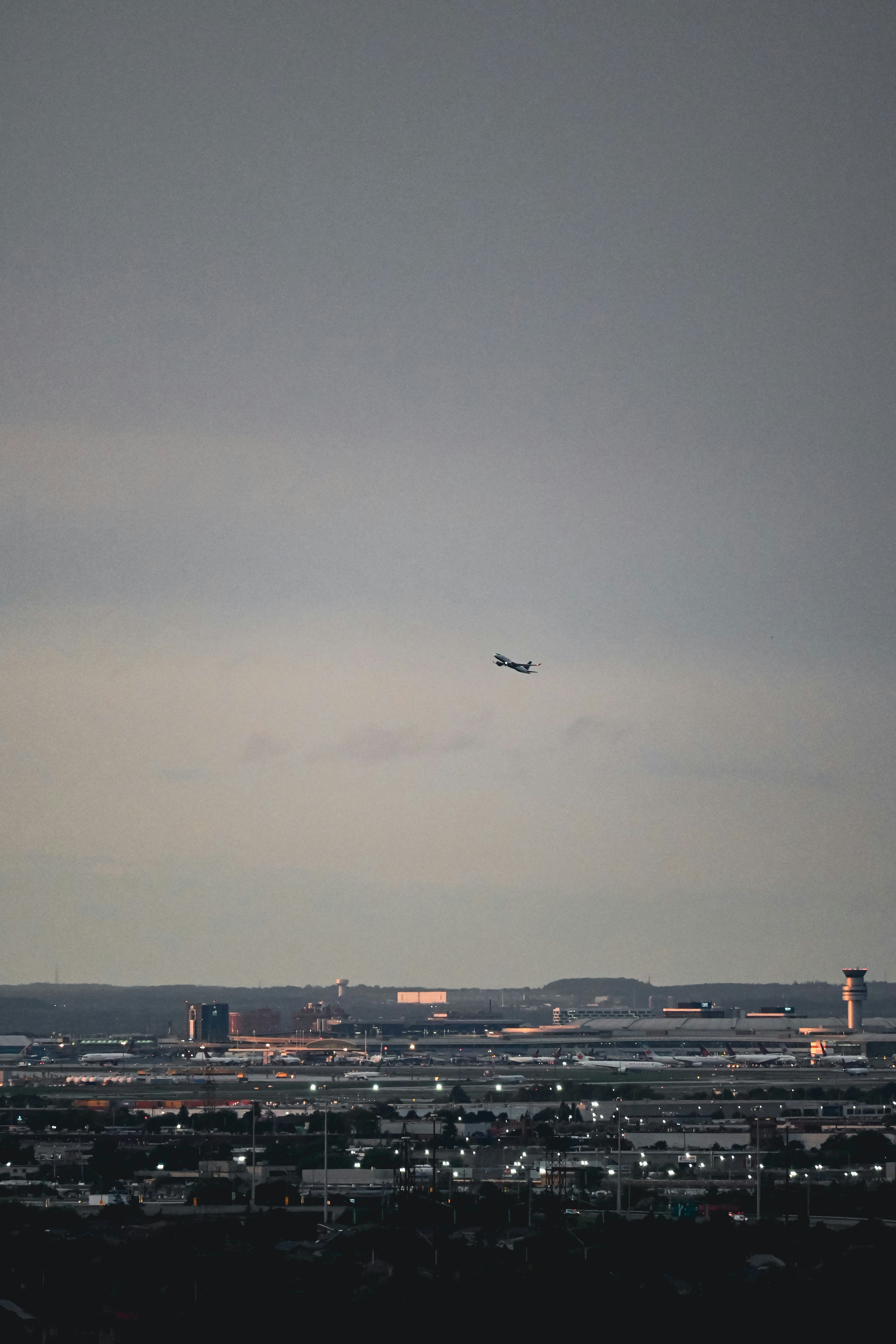 A lone departing aircraft cutting through layered twilight clouds above Toronto Pearson, with the airport lights quietly glowing below.