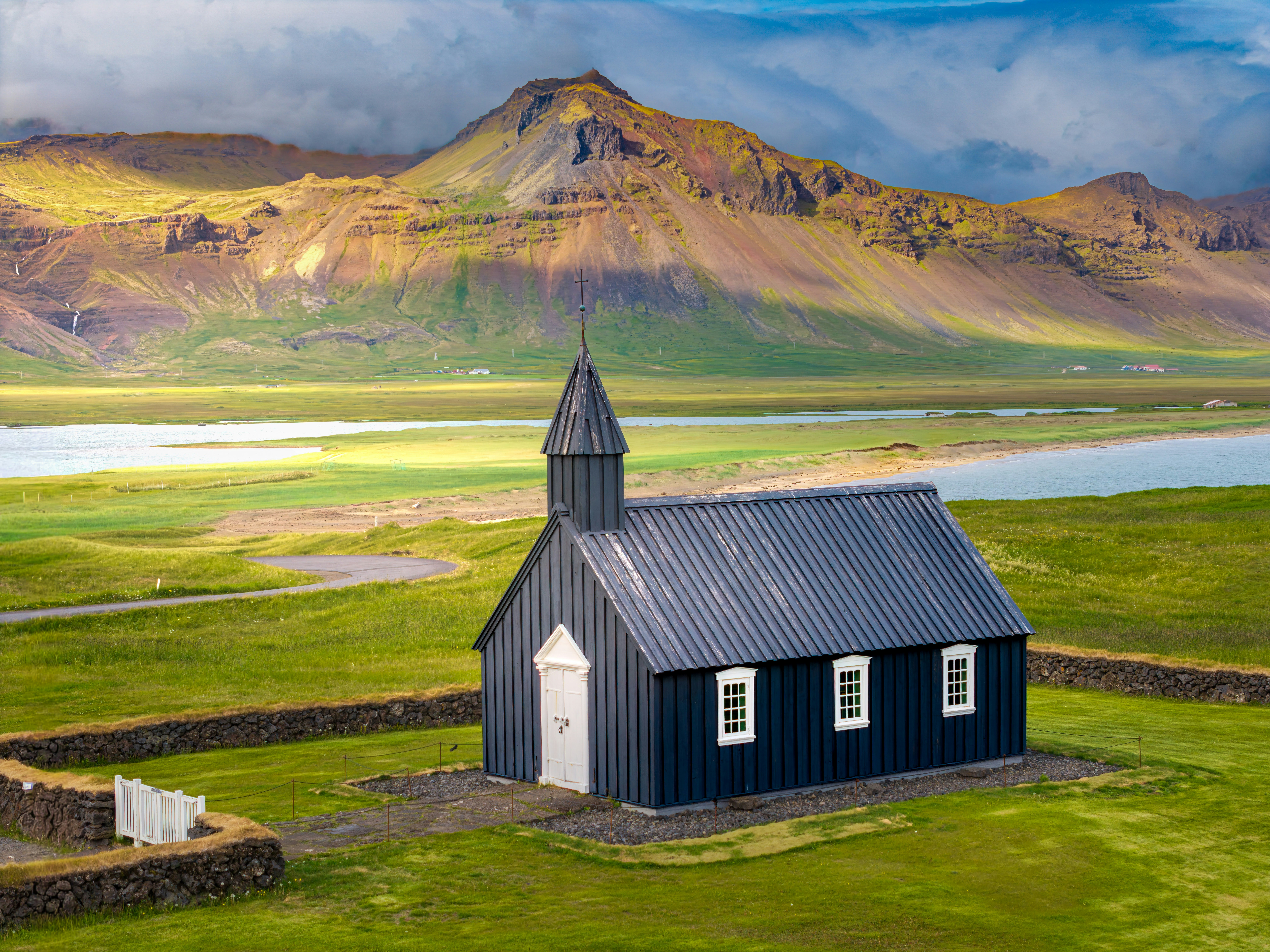 Blue chapel by a green valley under volcanic peaks