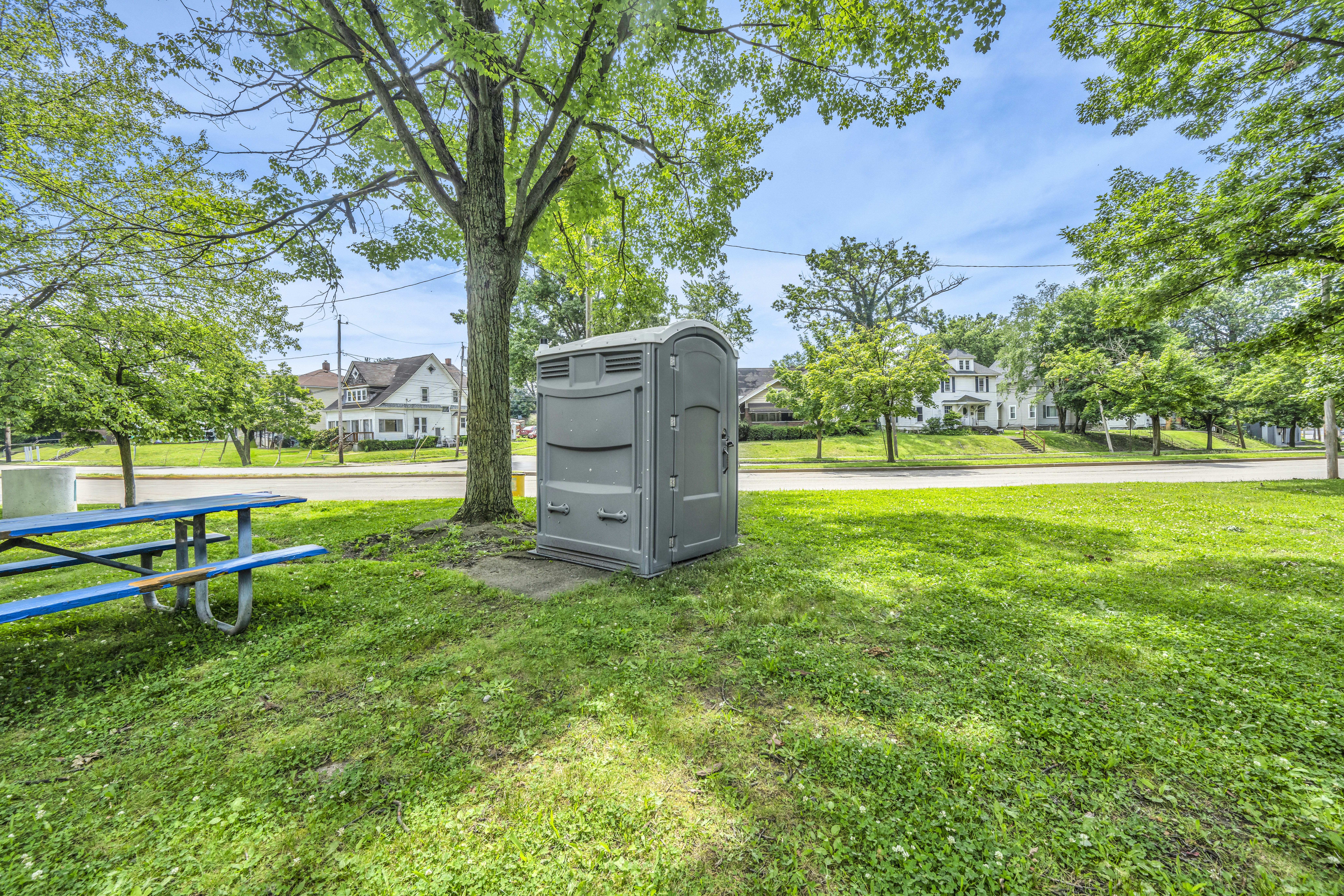 Portable Toilet in a Sunlit Park: A Quiet Moment Under Green Canopy