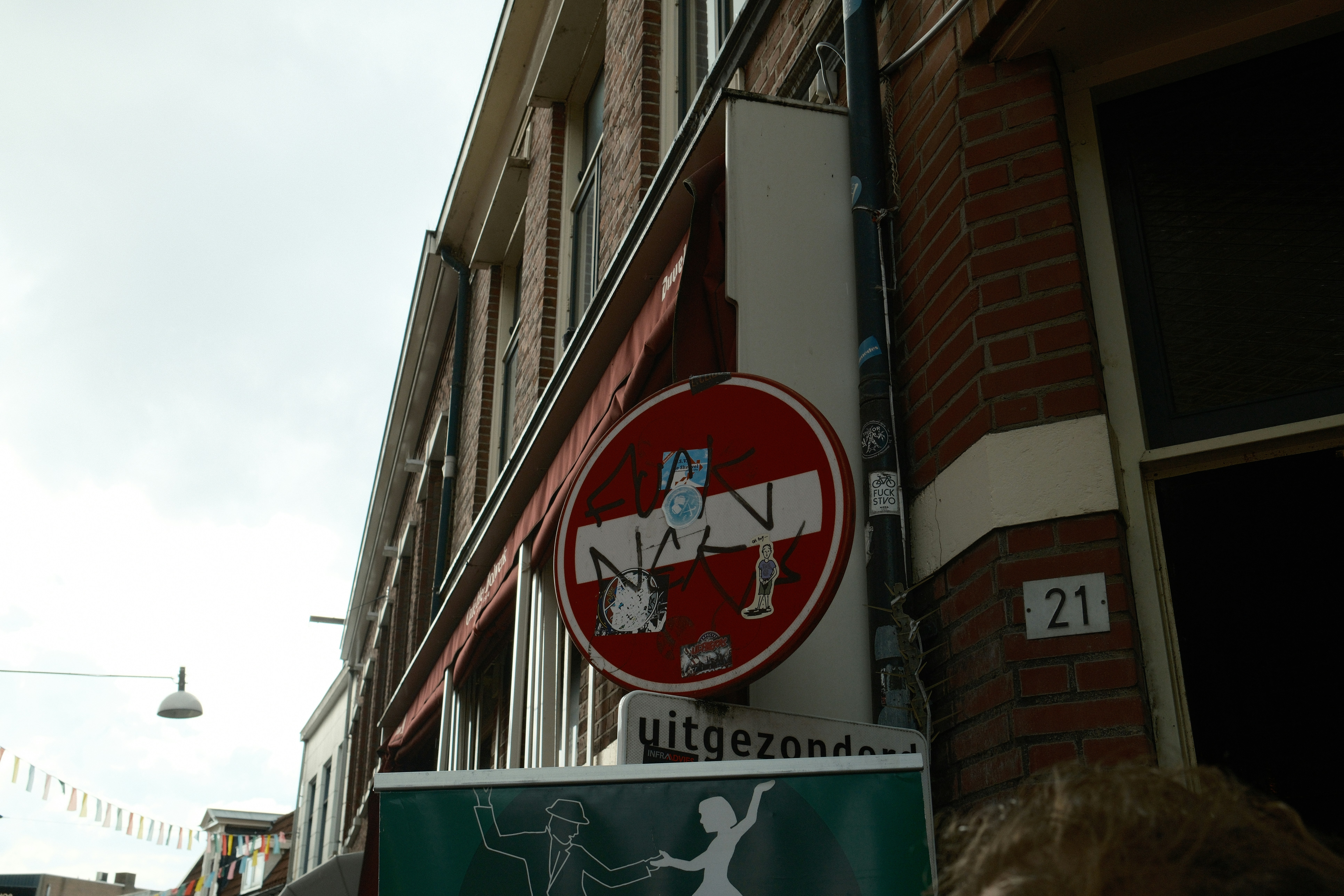 Tilted Red Circle Sign Above a Green Safety Banner on a City Street