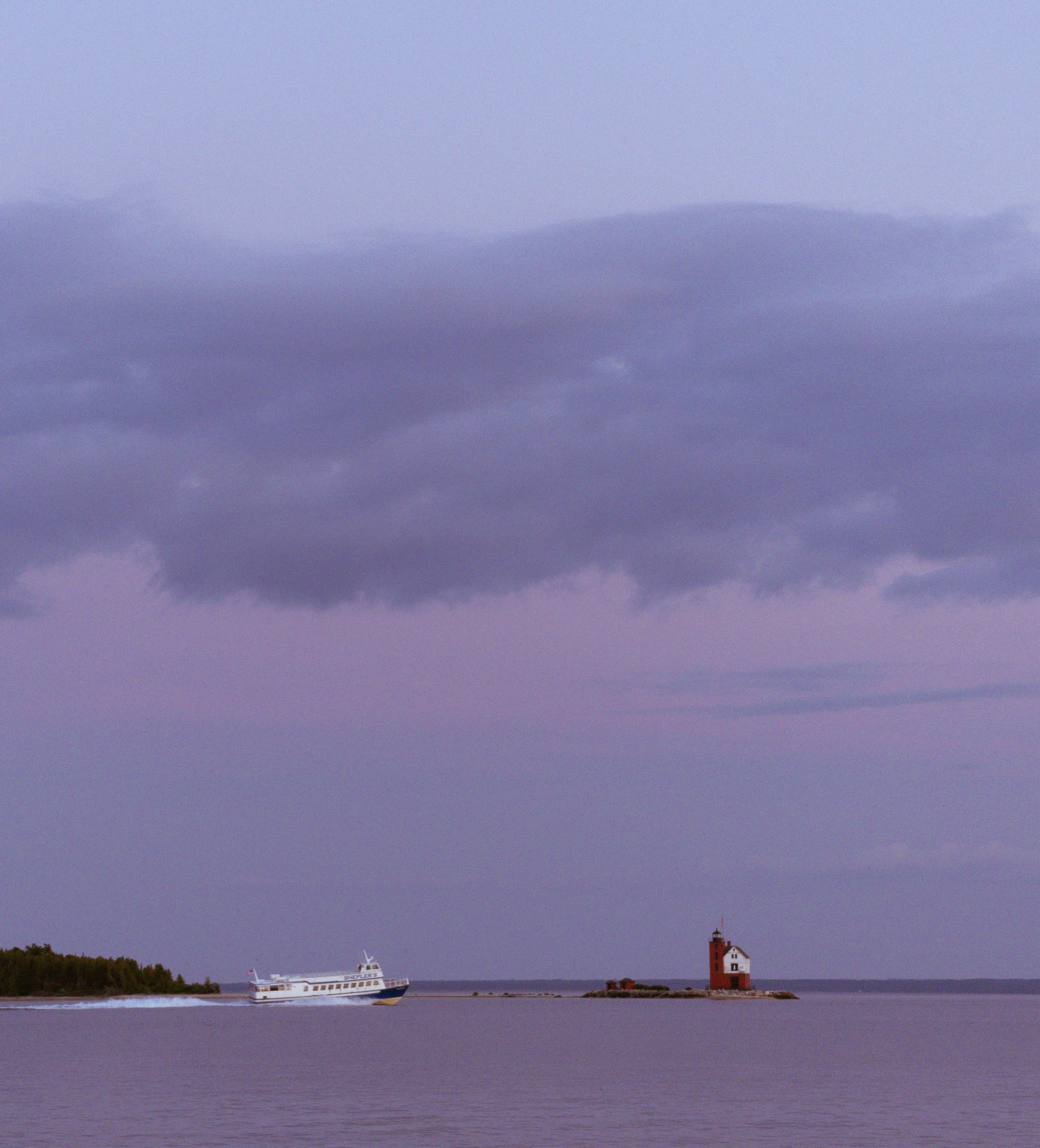 A lone lighthouse’s calm vigil: boat gliding toward dusk