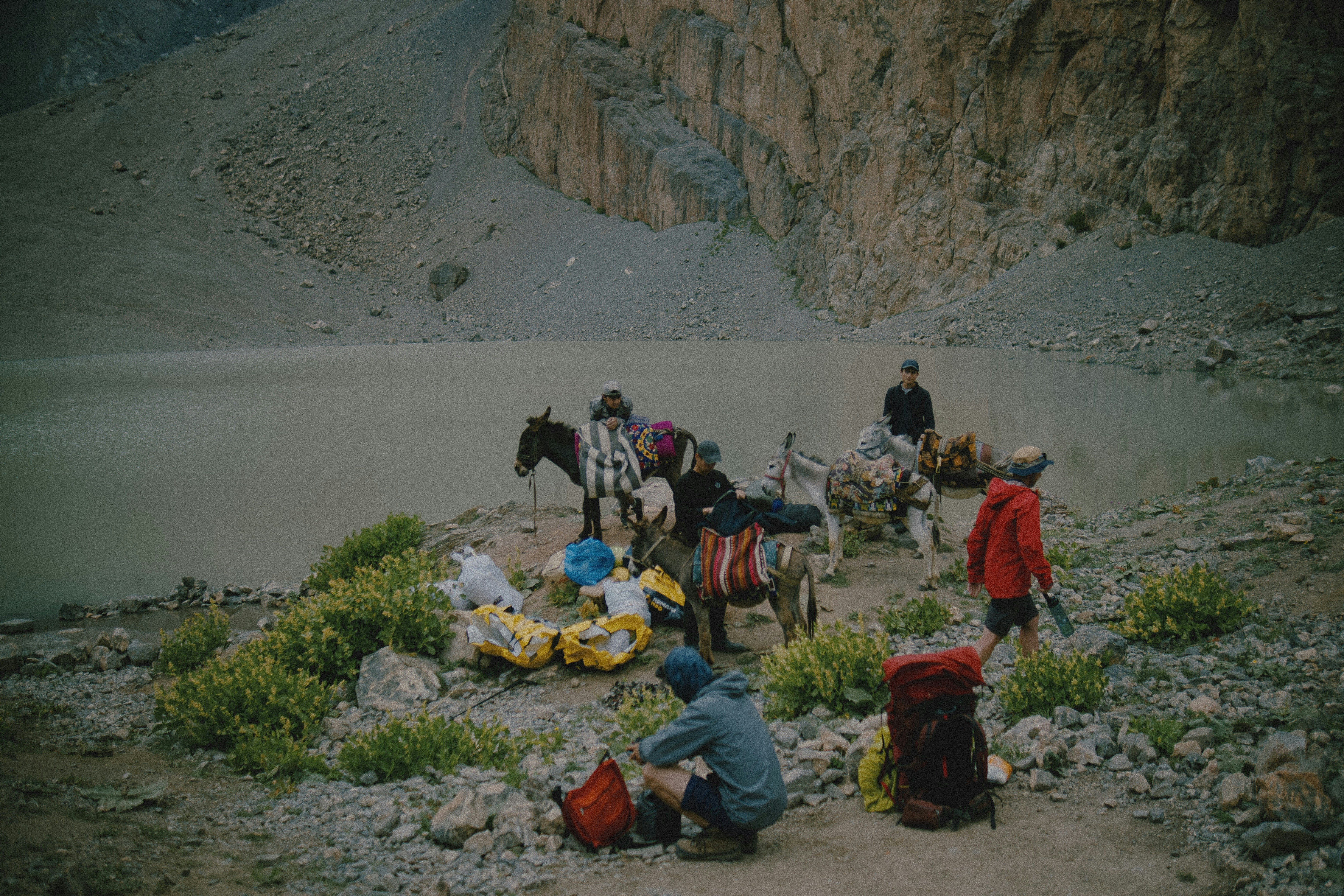 A group of people with pack animals and gear by a mountain lake