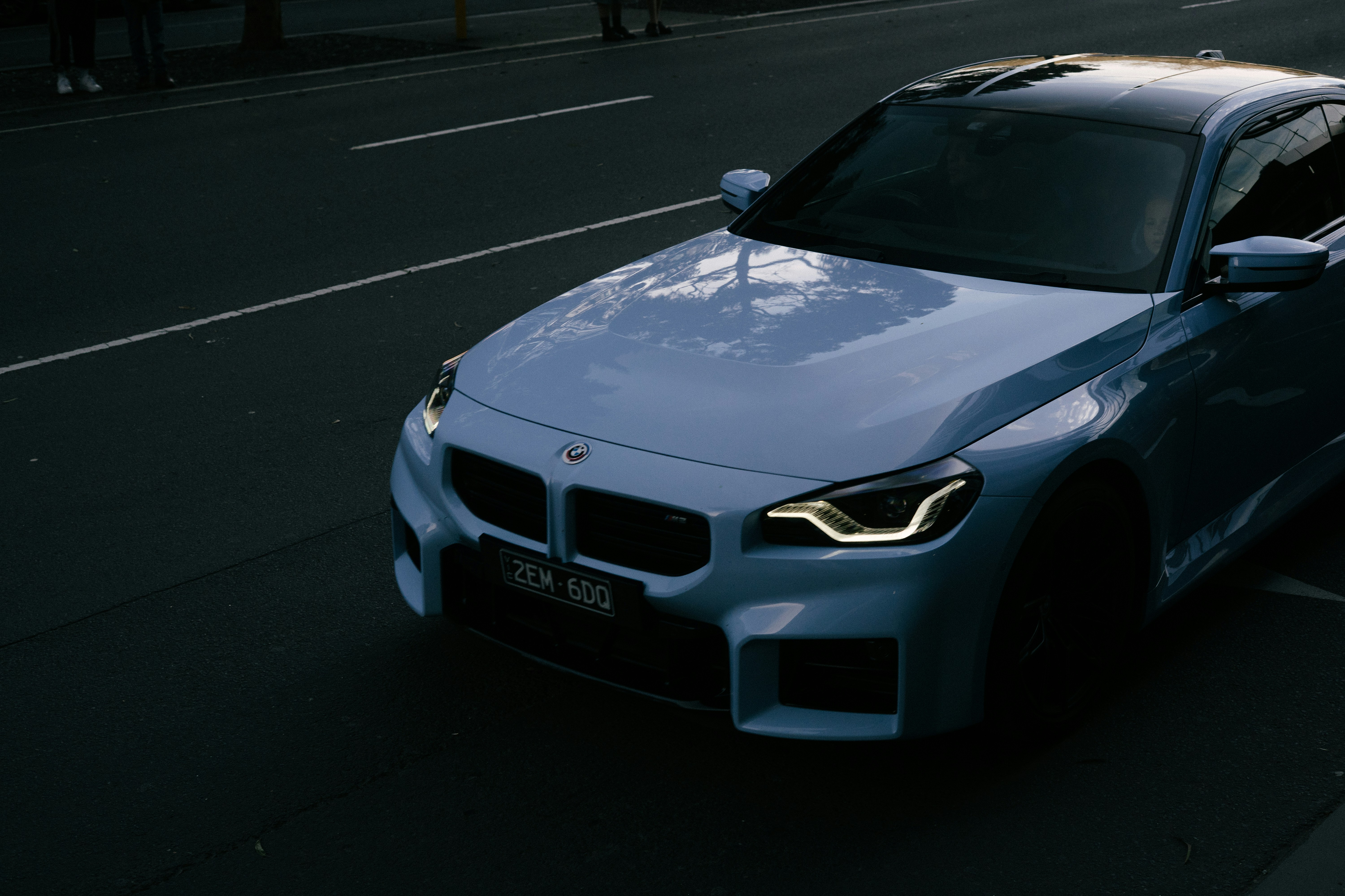Low-angle blue sedan on dim street with illuminated headlamps