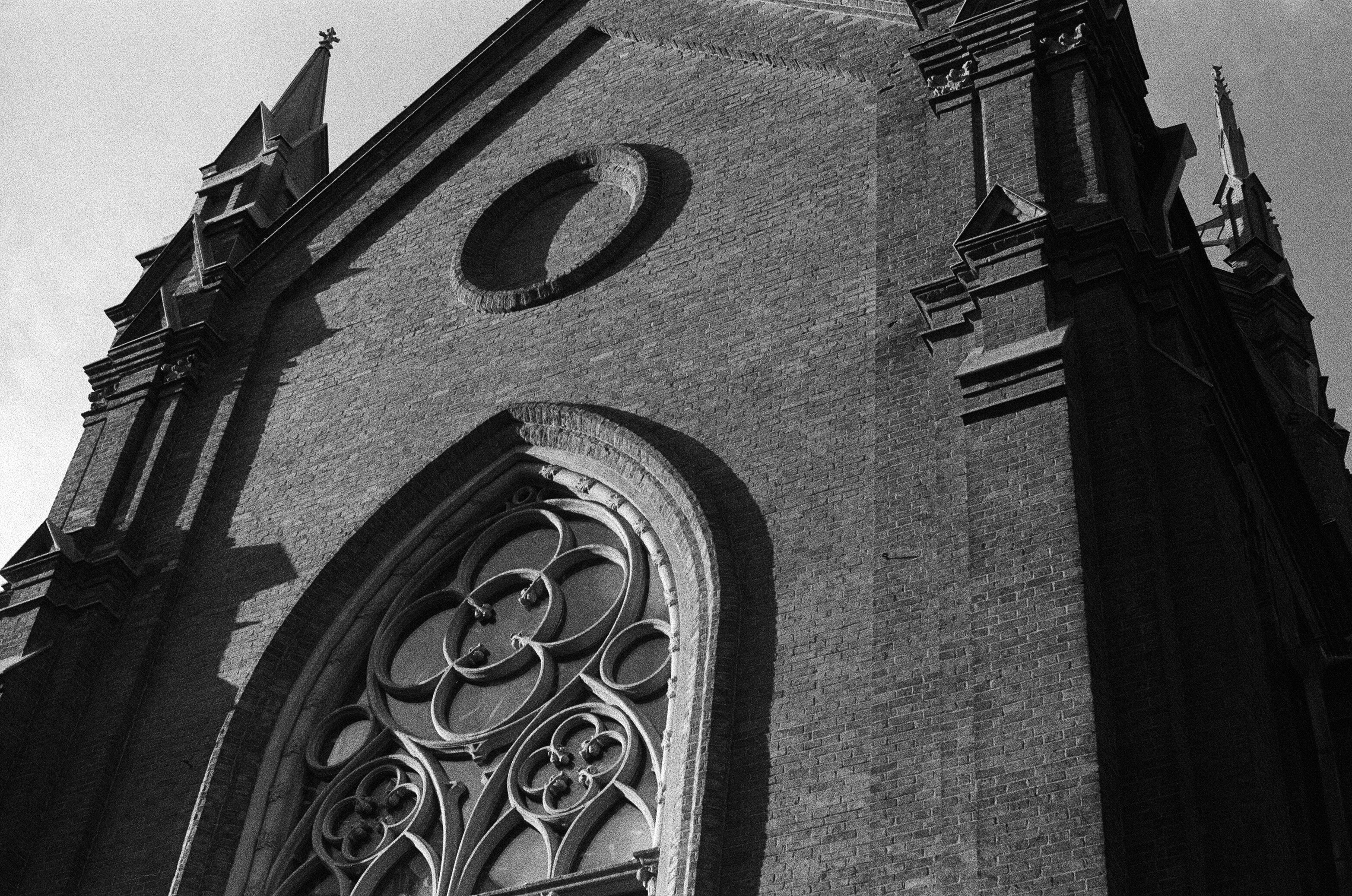Dark brick church facade with ornate circular window and rose window detailing, captured in grayscale to emphasize architectural textures.