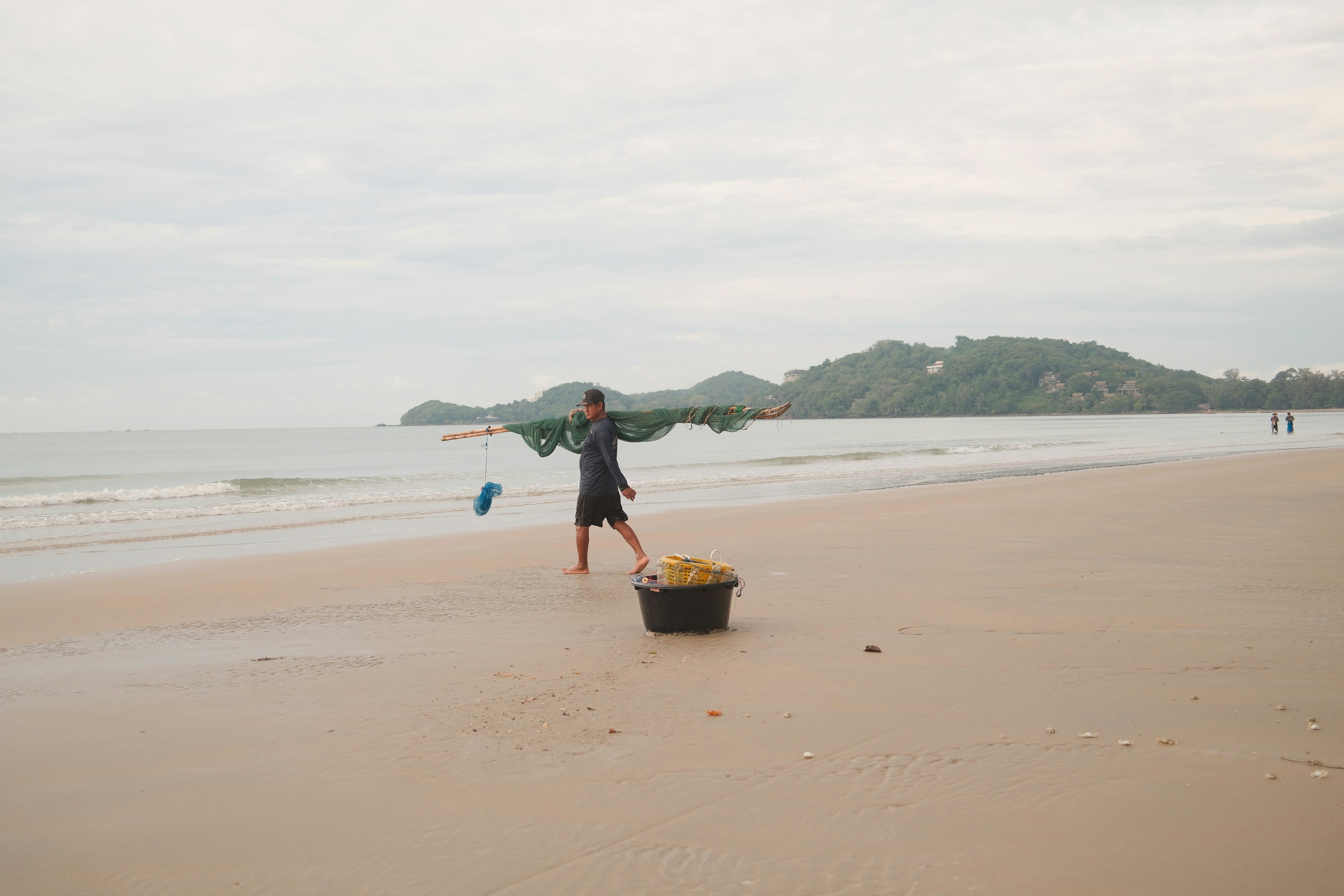 Beach Crier: A lone street vendor balances on the shoreline with a folded tarp