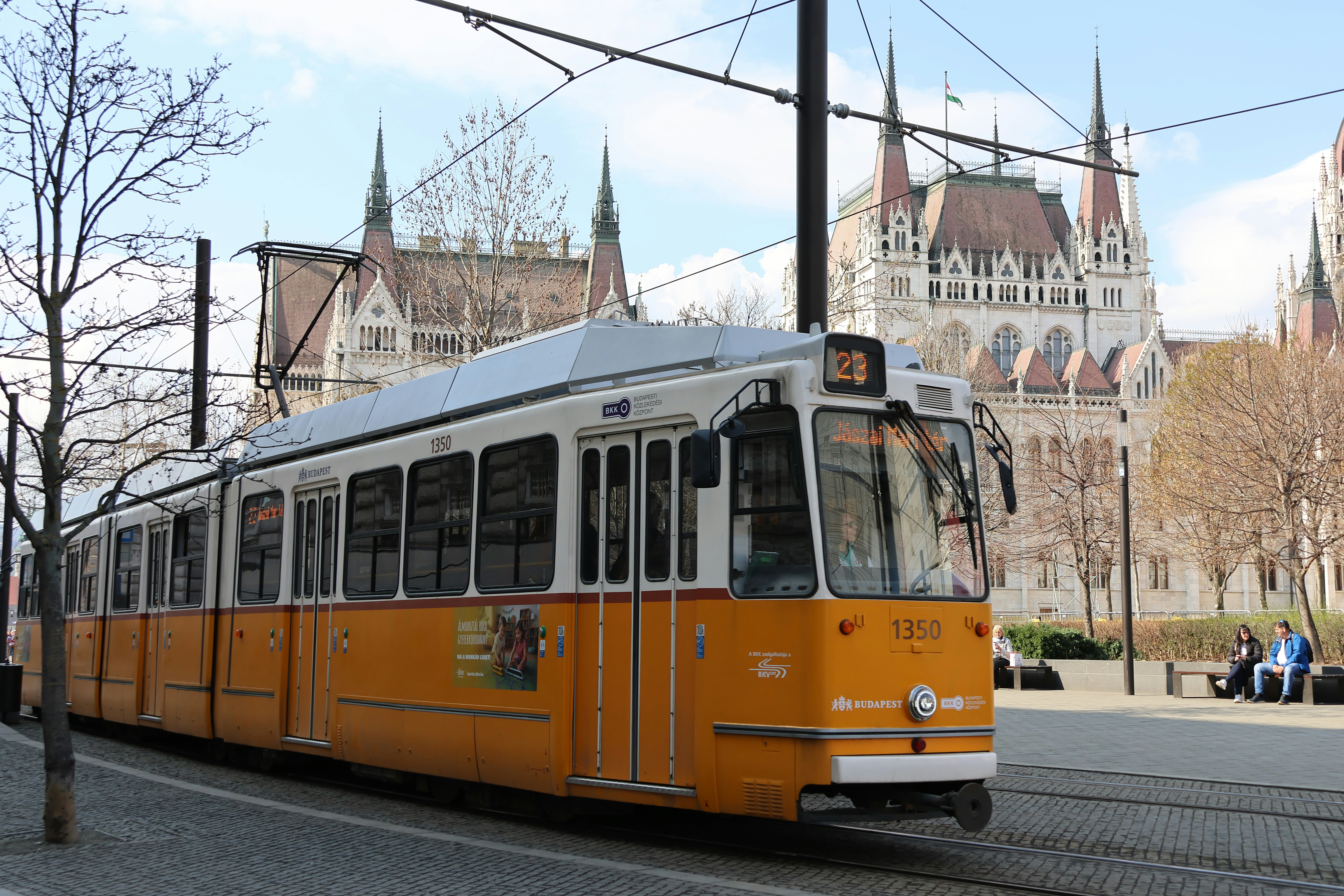 Bright yellow tram glides along a cobblestone street with historic spires in the background, capturing urban transit in motion.