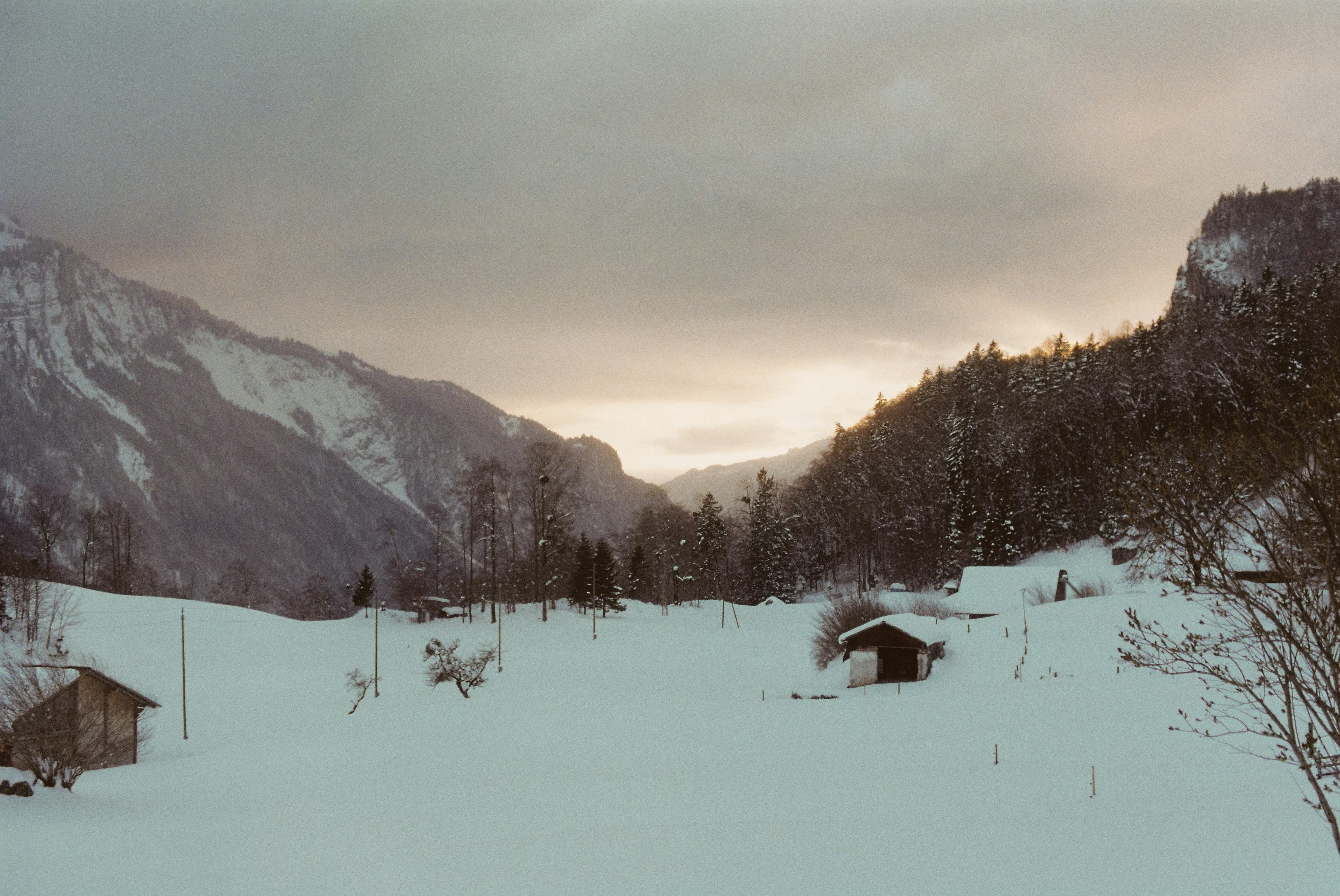 Snowbound valley at dusk with distant cabins and forested slopes
