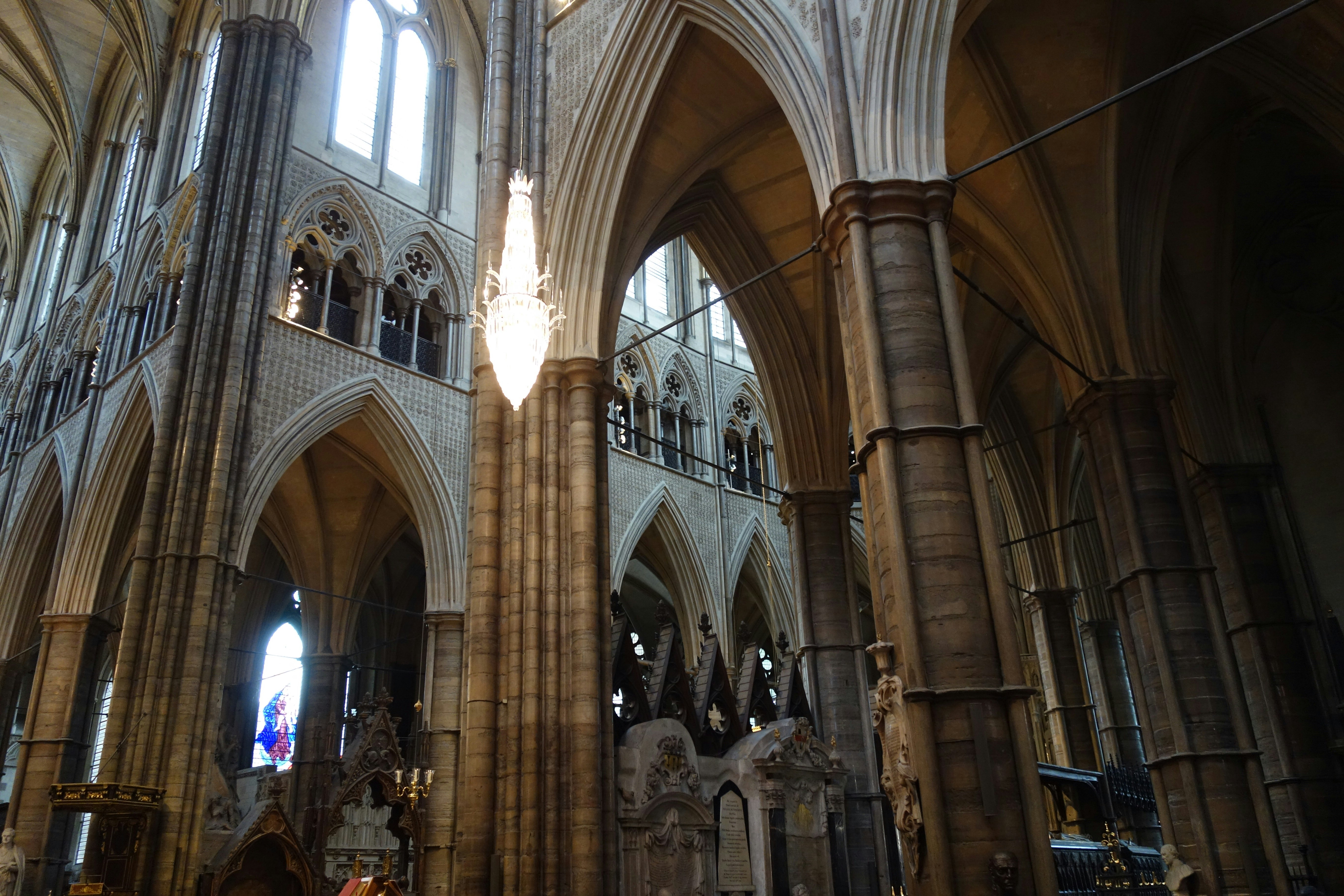 Inner Gothic cathedral arches and chandeliers bathed in warm light; stone columns rise toward ribbed vaults with figures visible in upper galleries.
