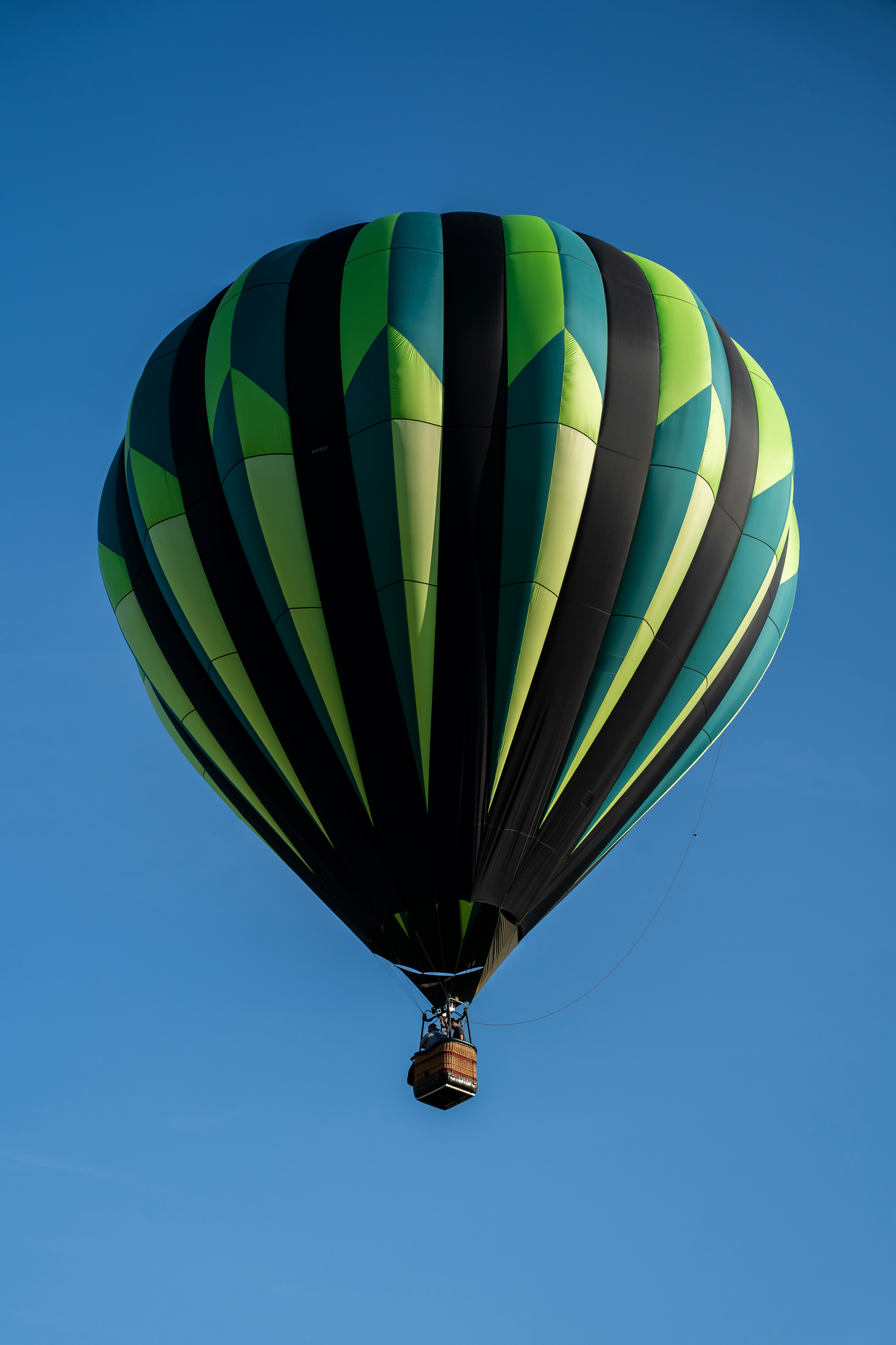 Neon-veined ascent: a lime-and-emerald hot air balloon rises against a clear blue sky