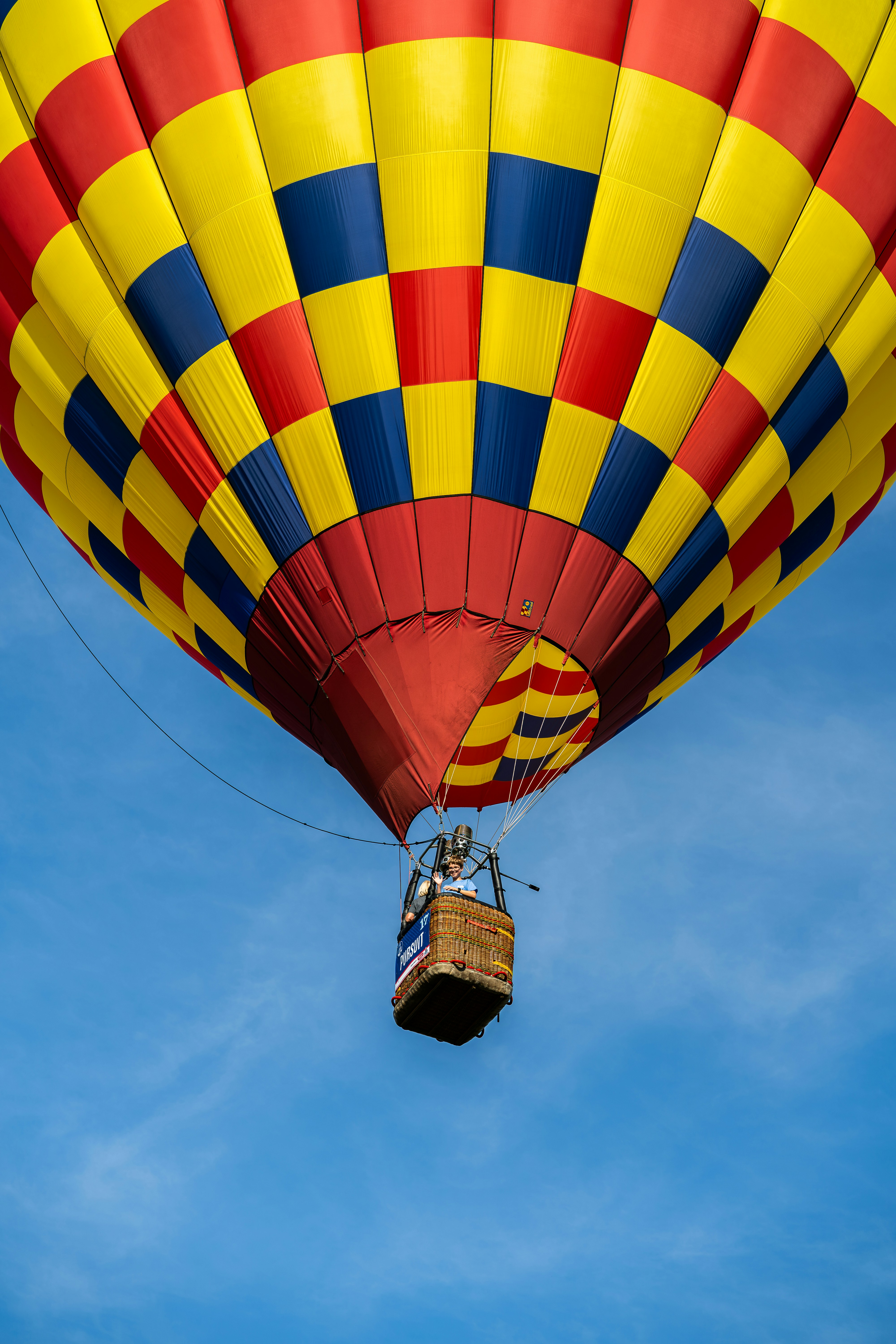 Low-angle ascent: a color-burst hot-air balloon lifting toward a clear blue sky