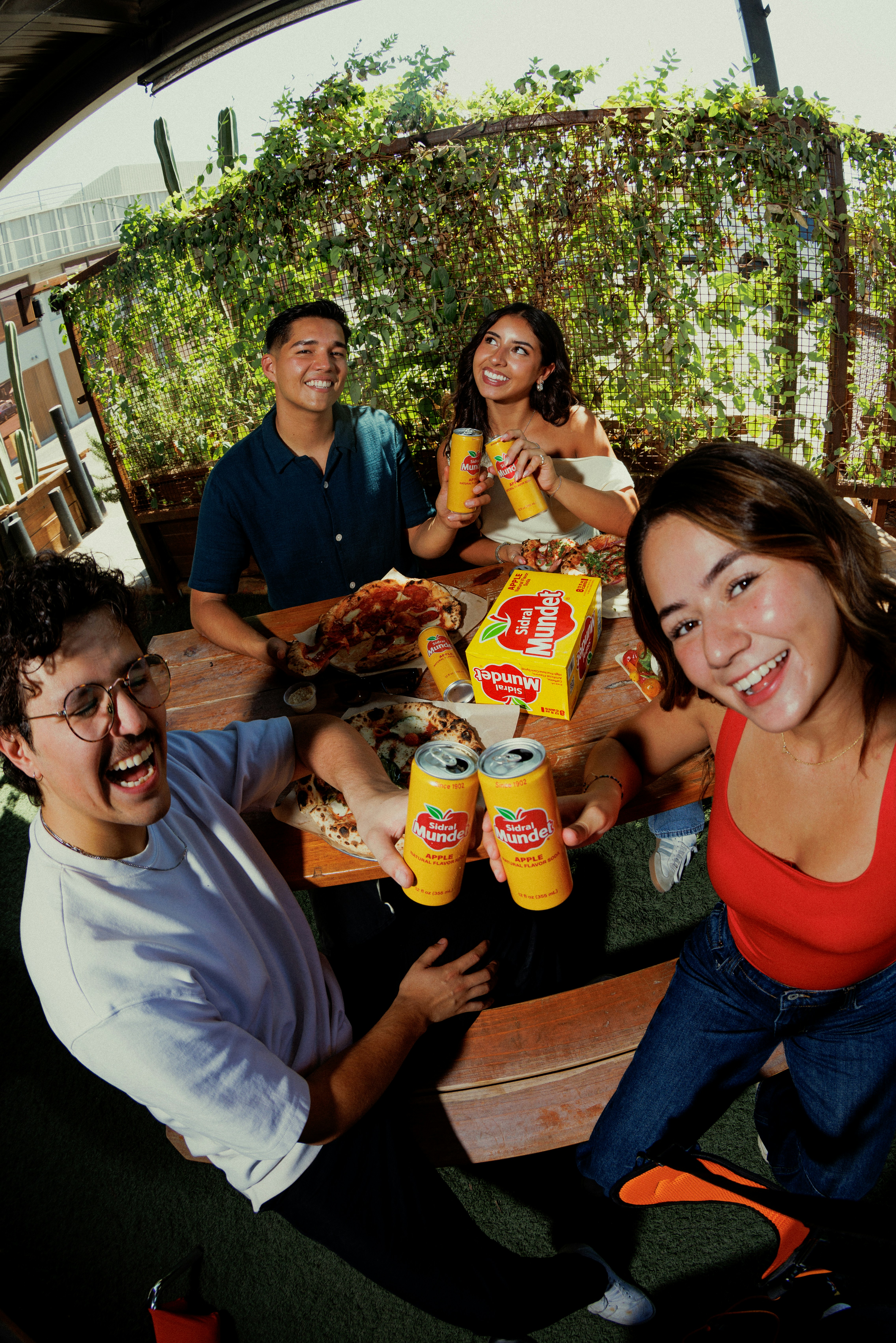 Cheerful rooftop feast: friends toast with cans of Munda in summer glow