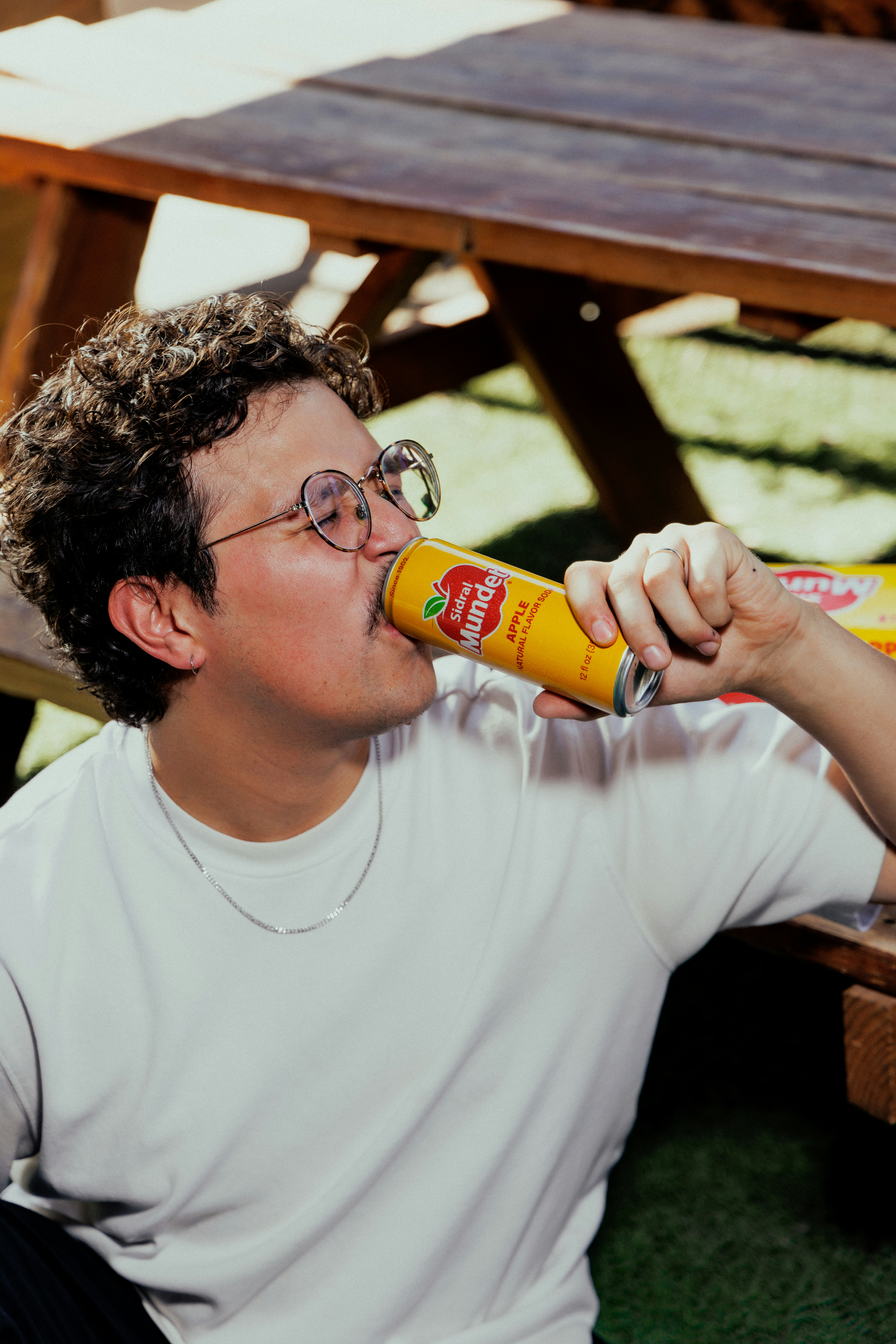 Sips and sunlight: a casual sip from a can under picnic shade