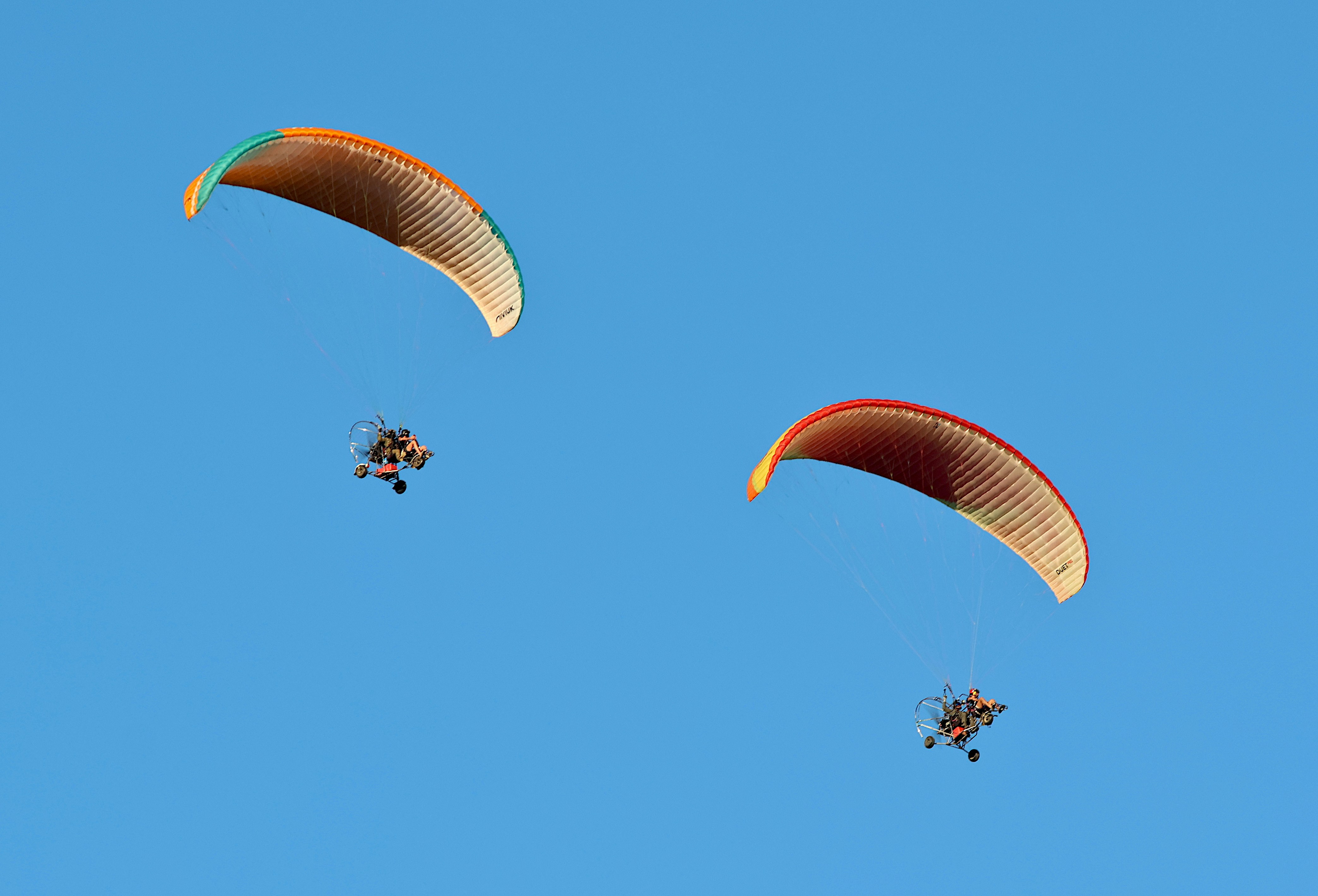Dual Paraglider Duo Skimming a Cloudless Blue Stage