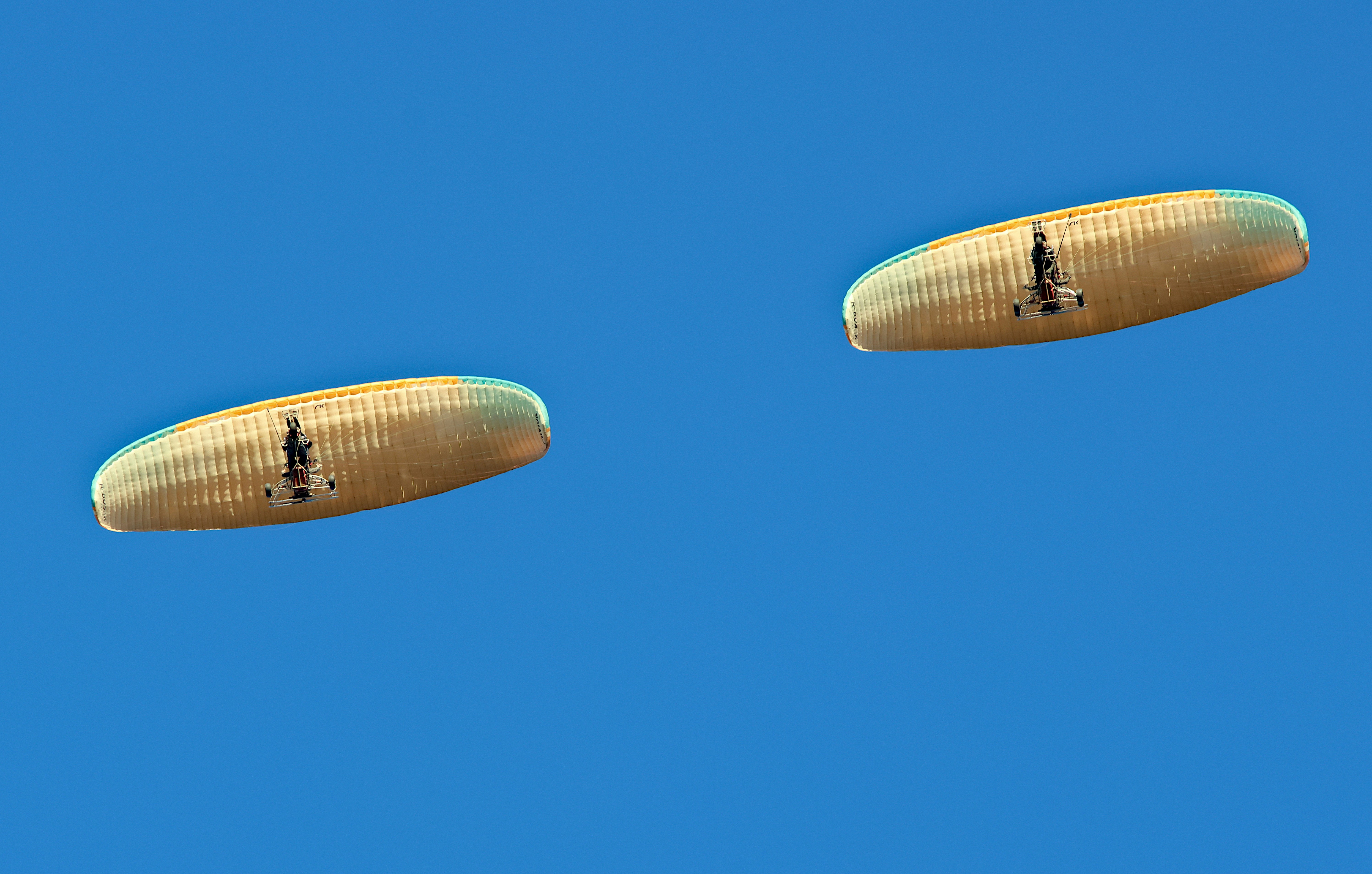 Twin Paragliders Cut Across a Vivid Blue Sky