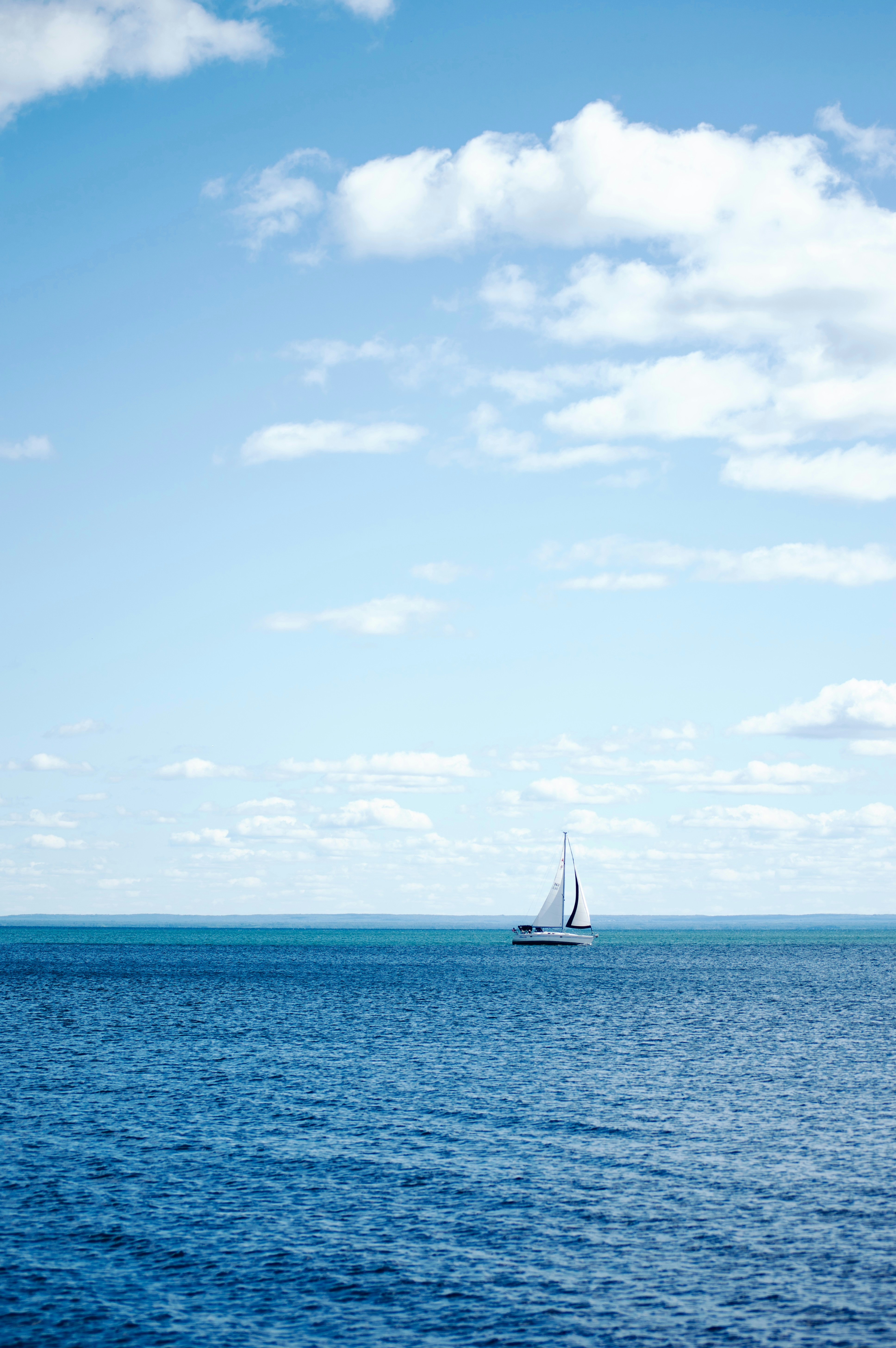 Sails on the Horizon: A Lone Sailboat Crossing a Blue Expanse