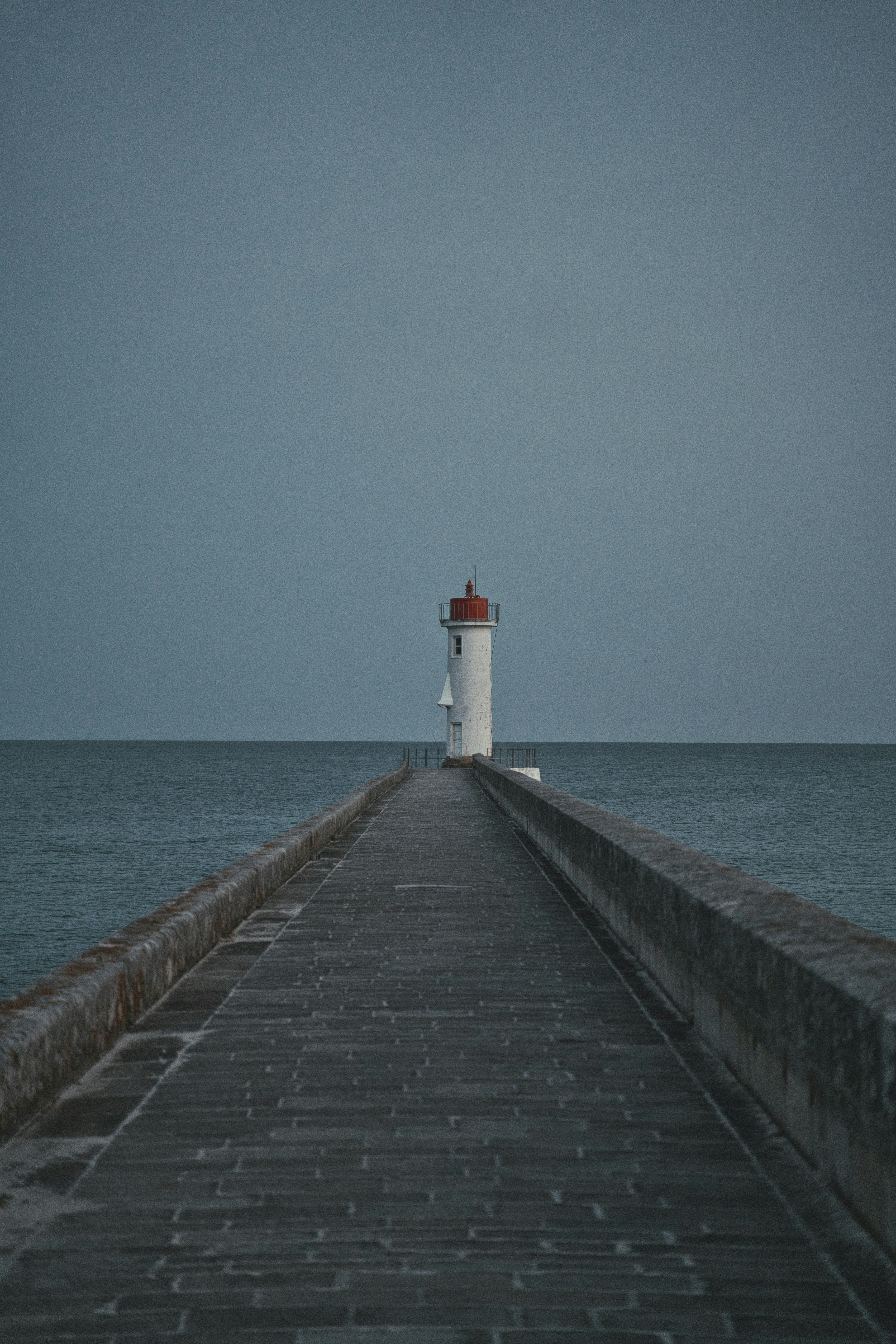 Endless Pier to a White Lighthouse Under Quiet Skies