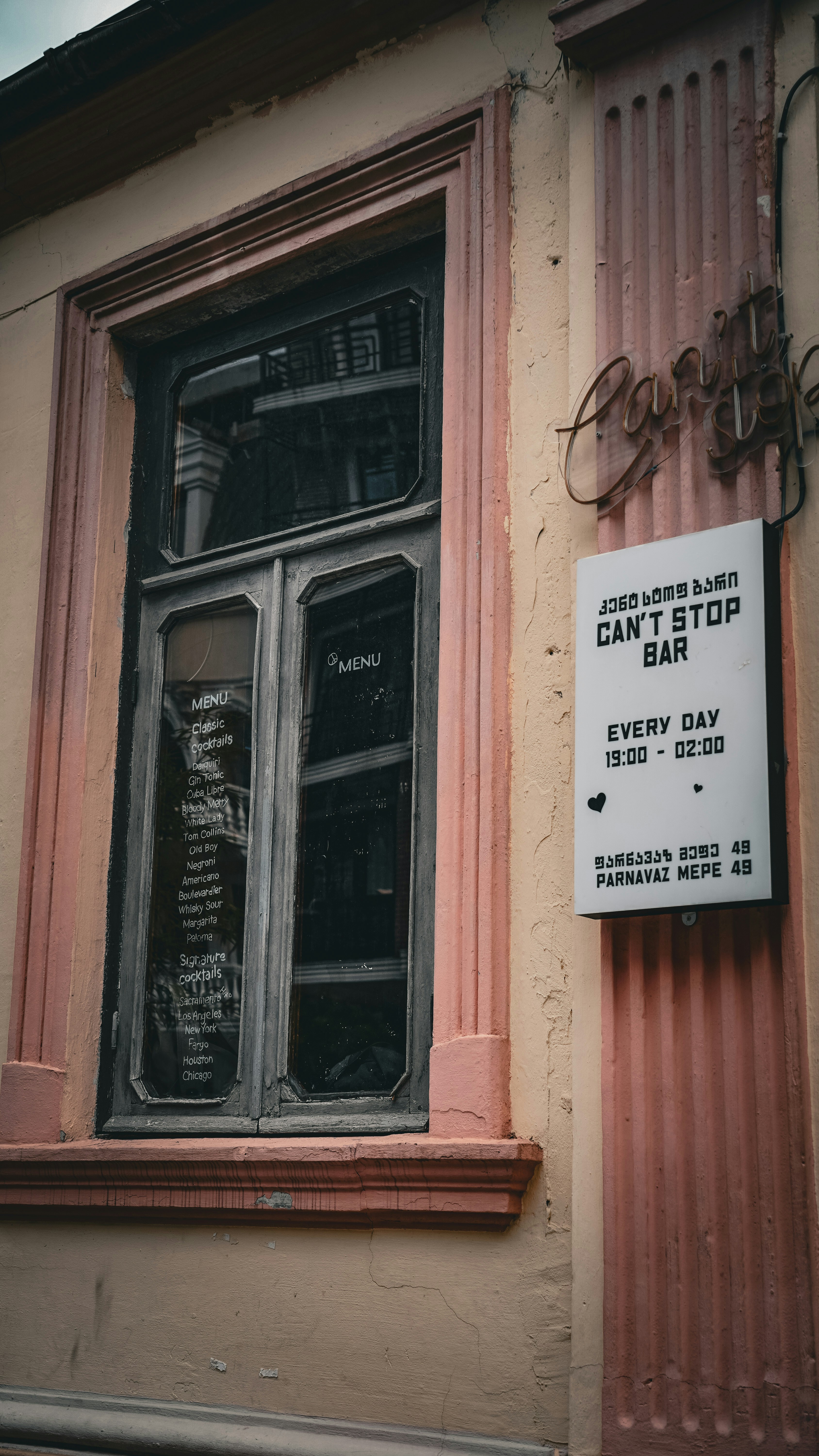 A window with a menu and a sign reading Can't Stop Bar on a building