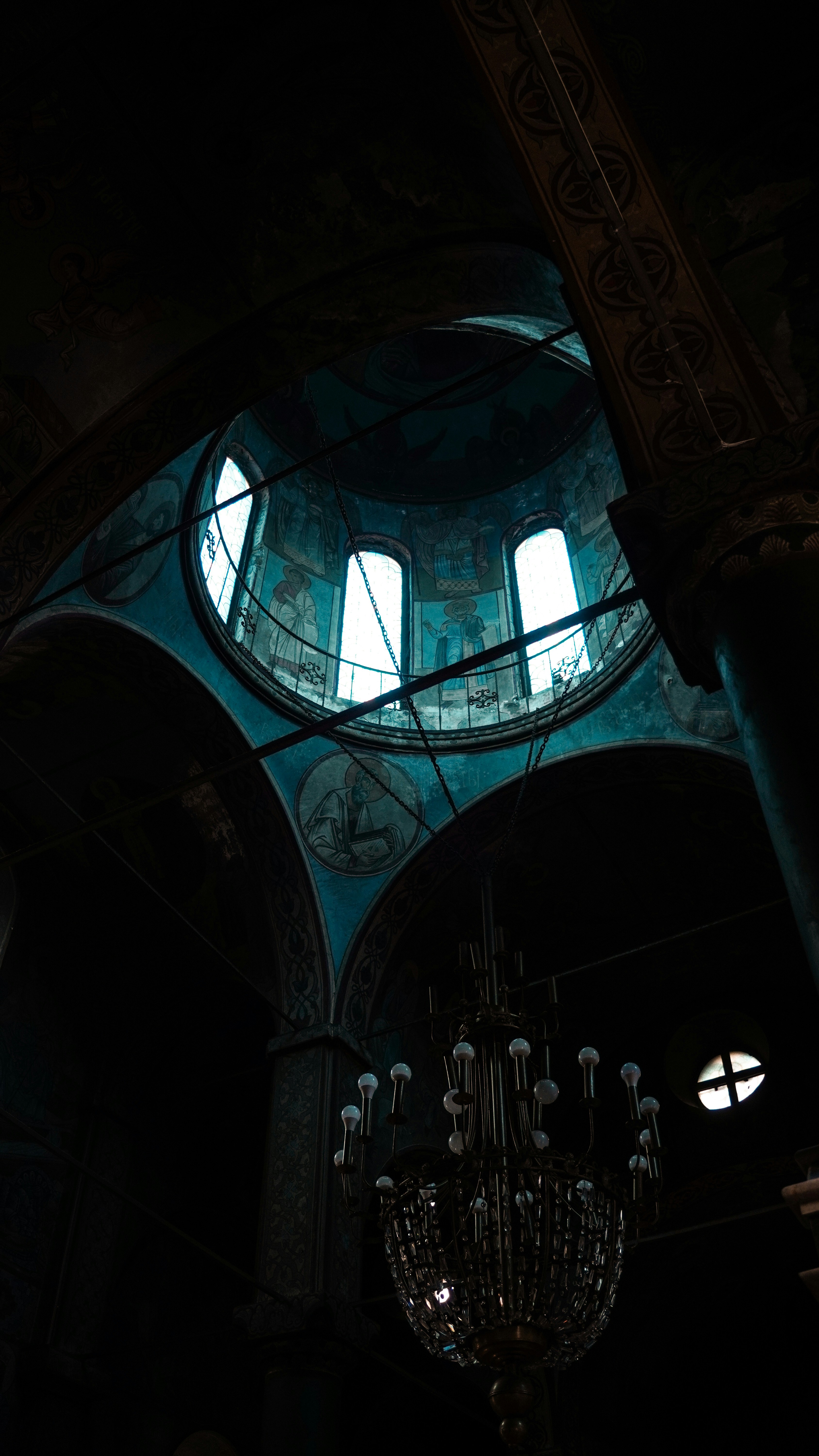 A dim church interior with a large crystal chandelier beneath a painted dome