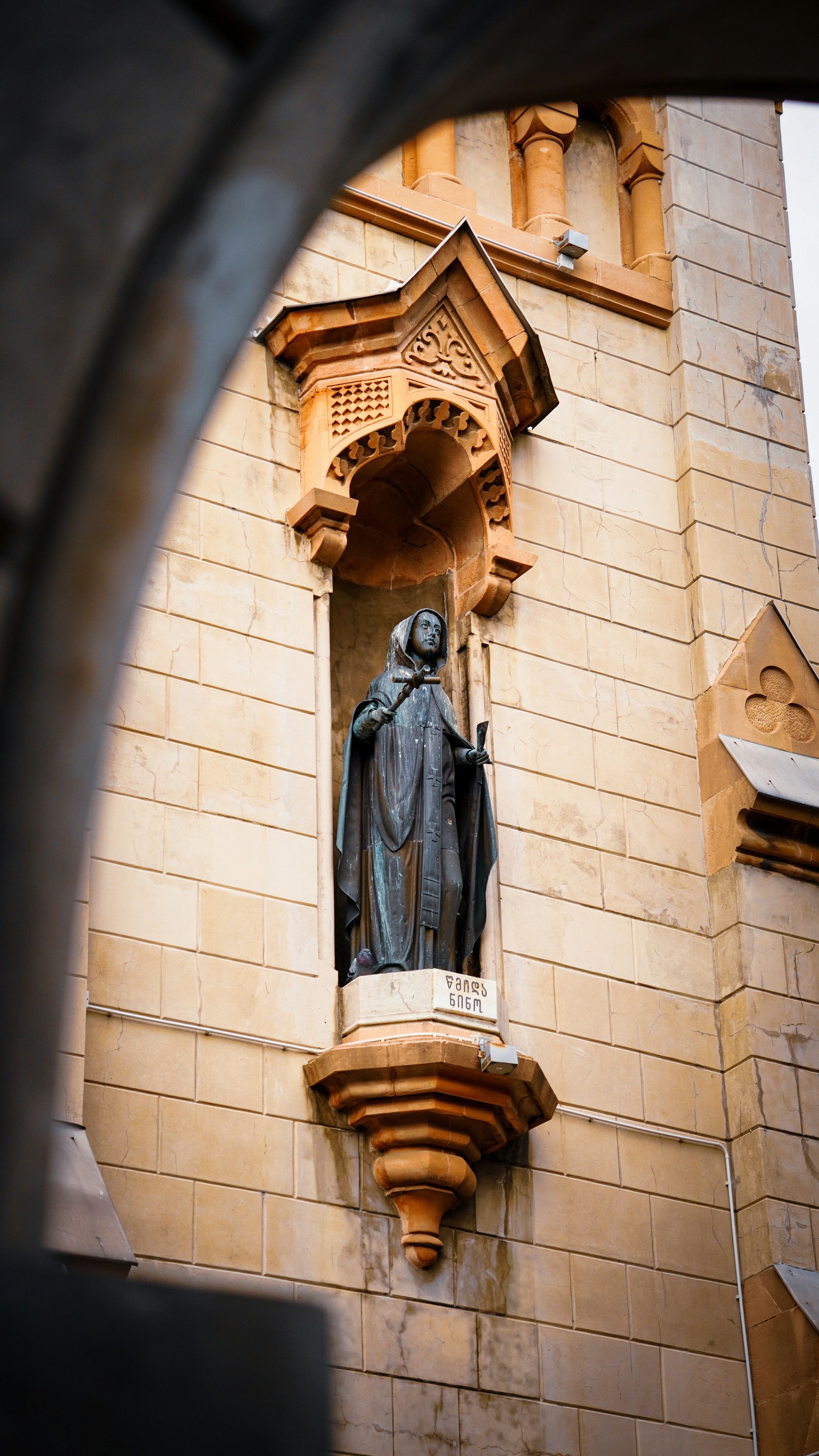A bronze statue of a robed figure holding a cross in a stone niche