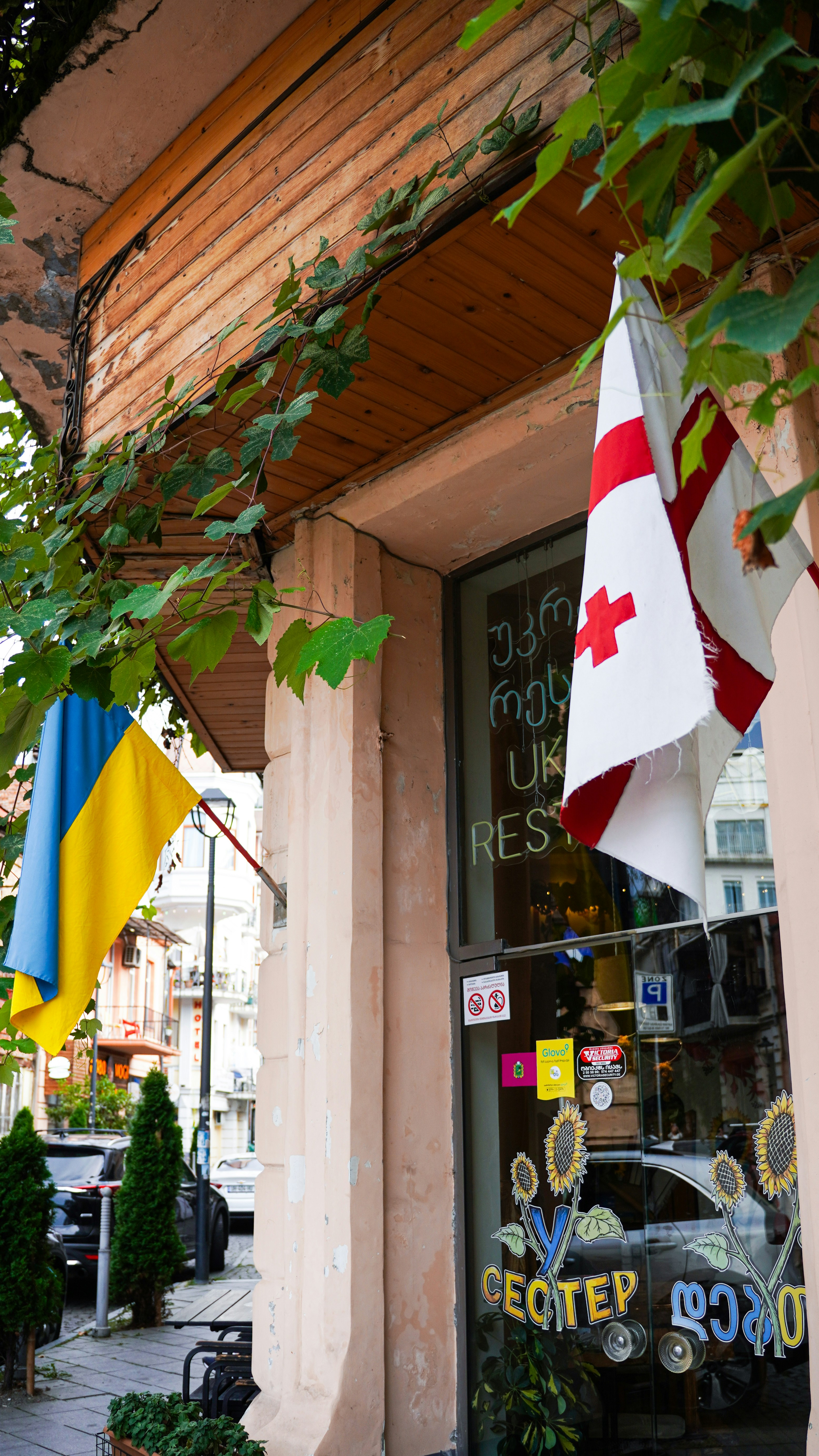 The flags of Ukraine and Georgia hanging outside a restaurant entrance with sunflower decals