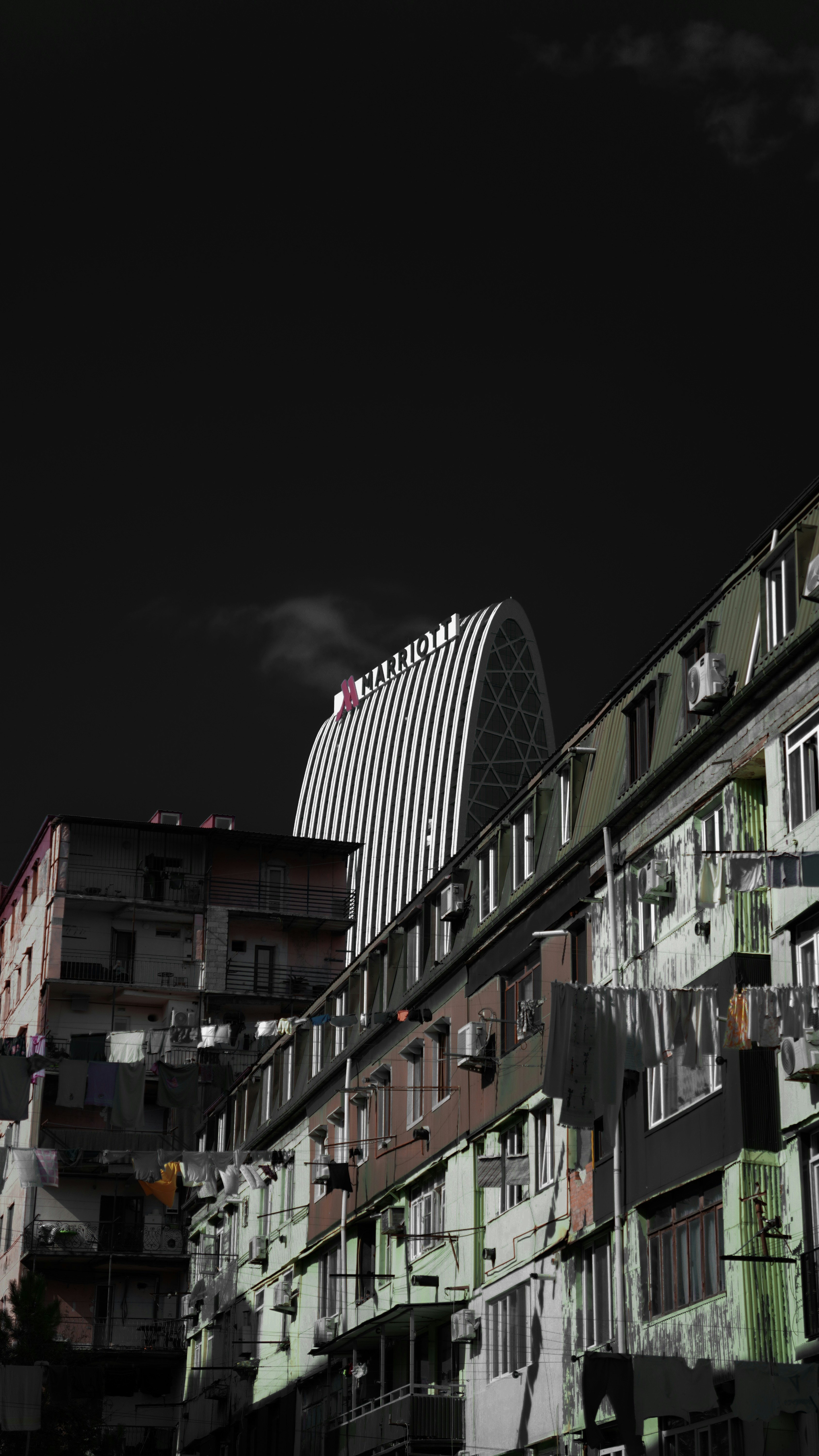 A modern Marriott hotel tower rising behind weathered apartment buildings with laundry hanging outside