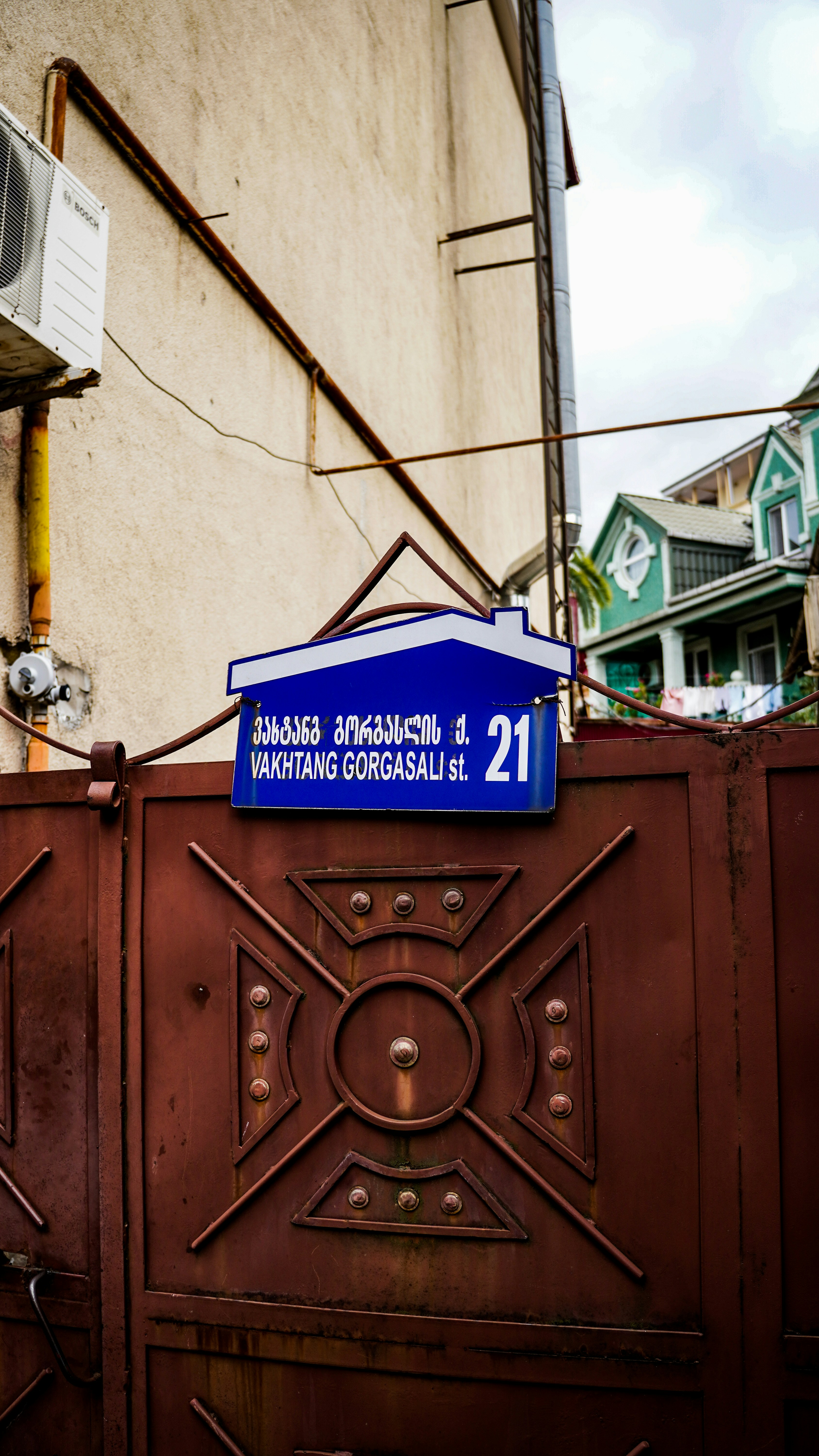 A blue street sign reading Vakhtang Gorgasali st 21 on a brown metal gate