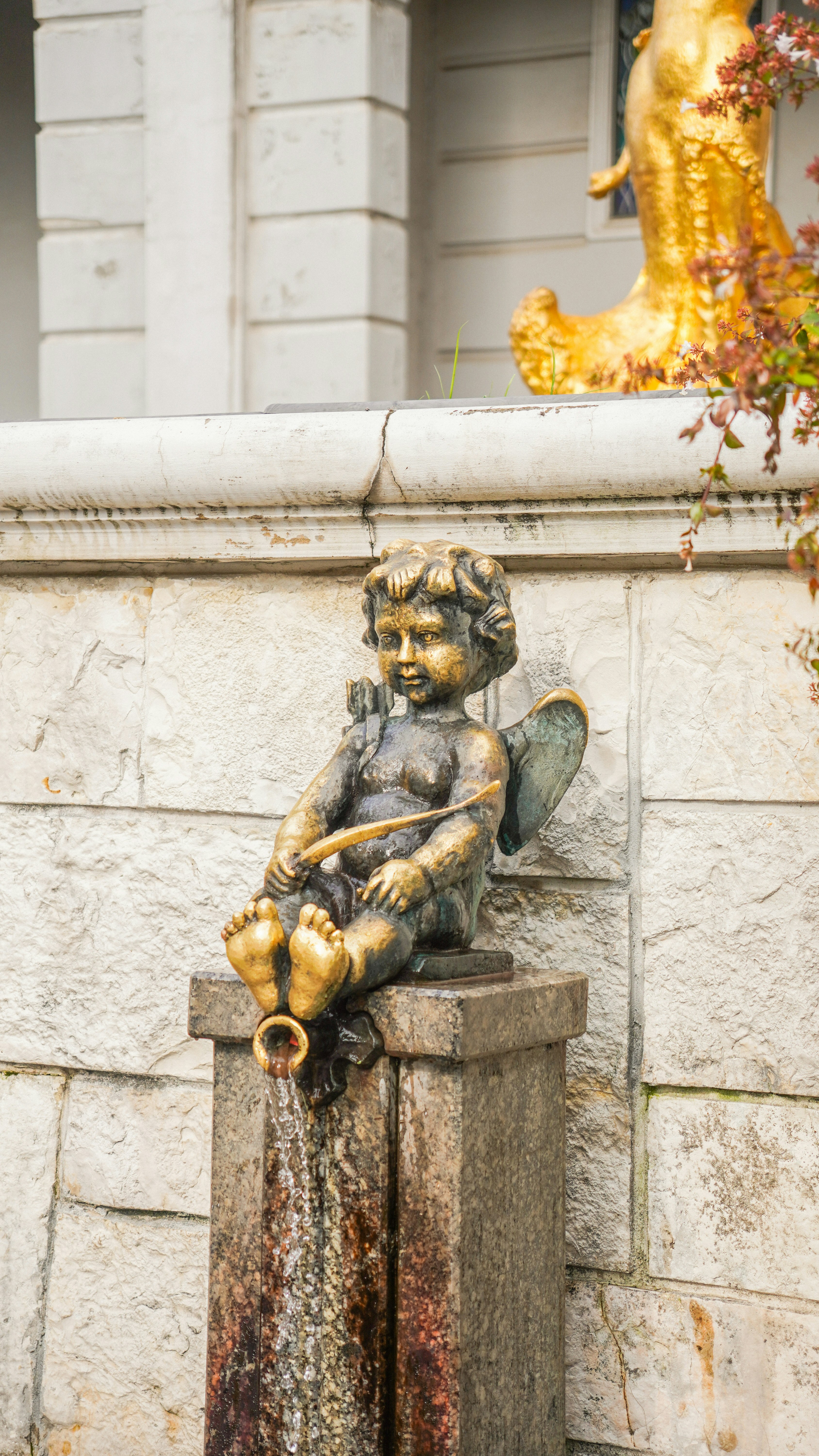 A bronze cherub fountain statue pouring water from a small spout on a pedestal