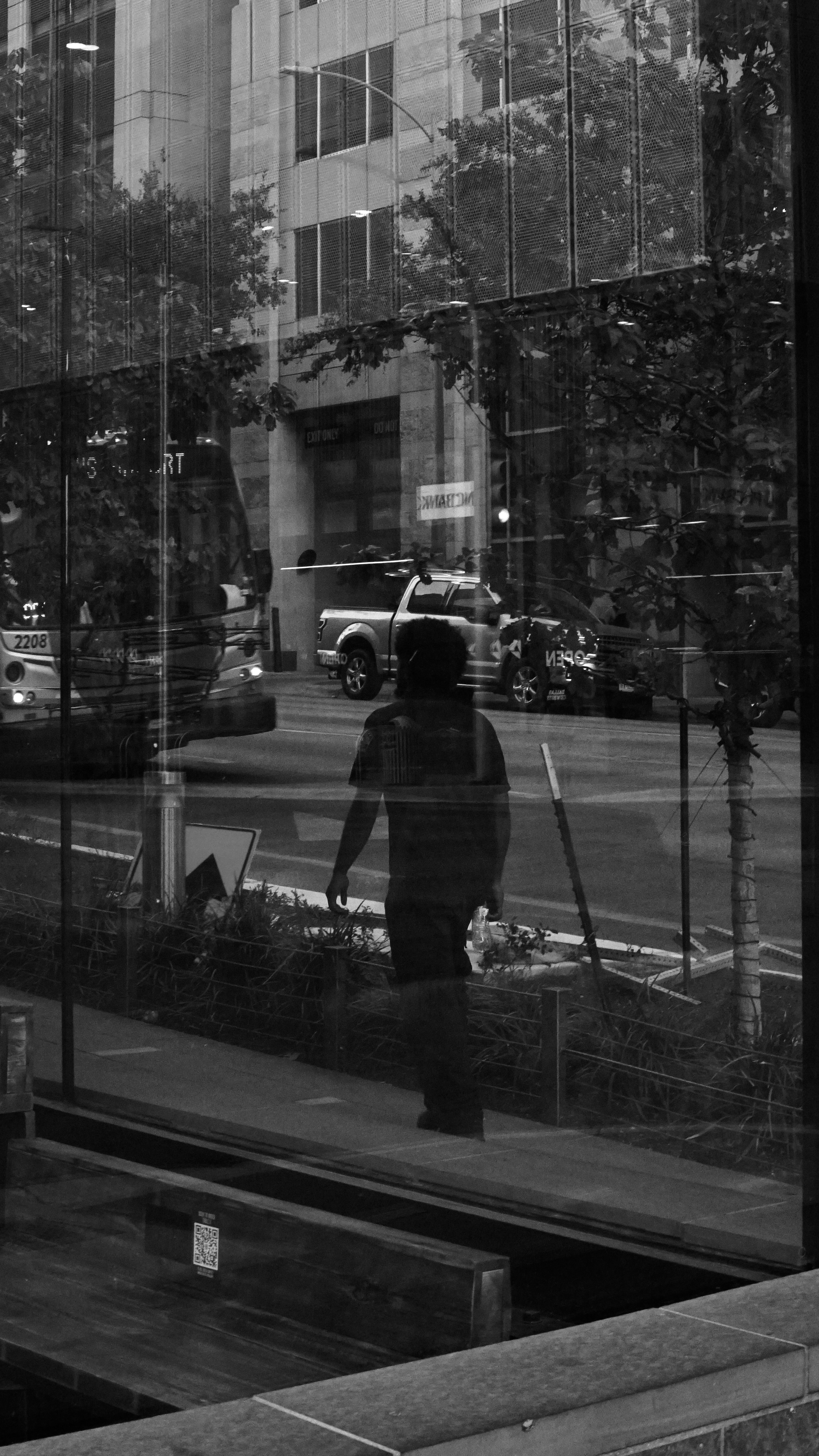 Reflected silhouettes: a lone passerby through glass urban tides