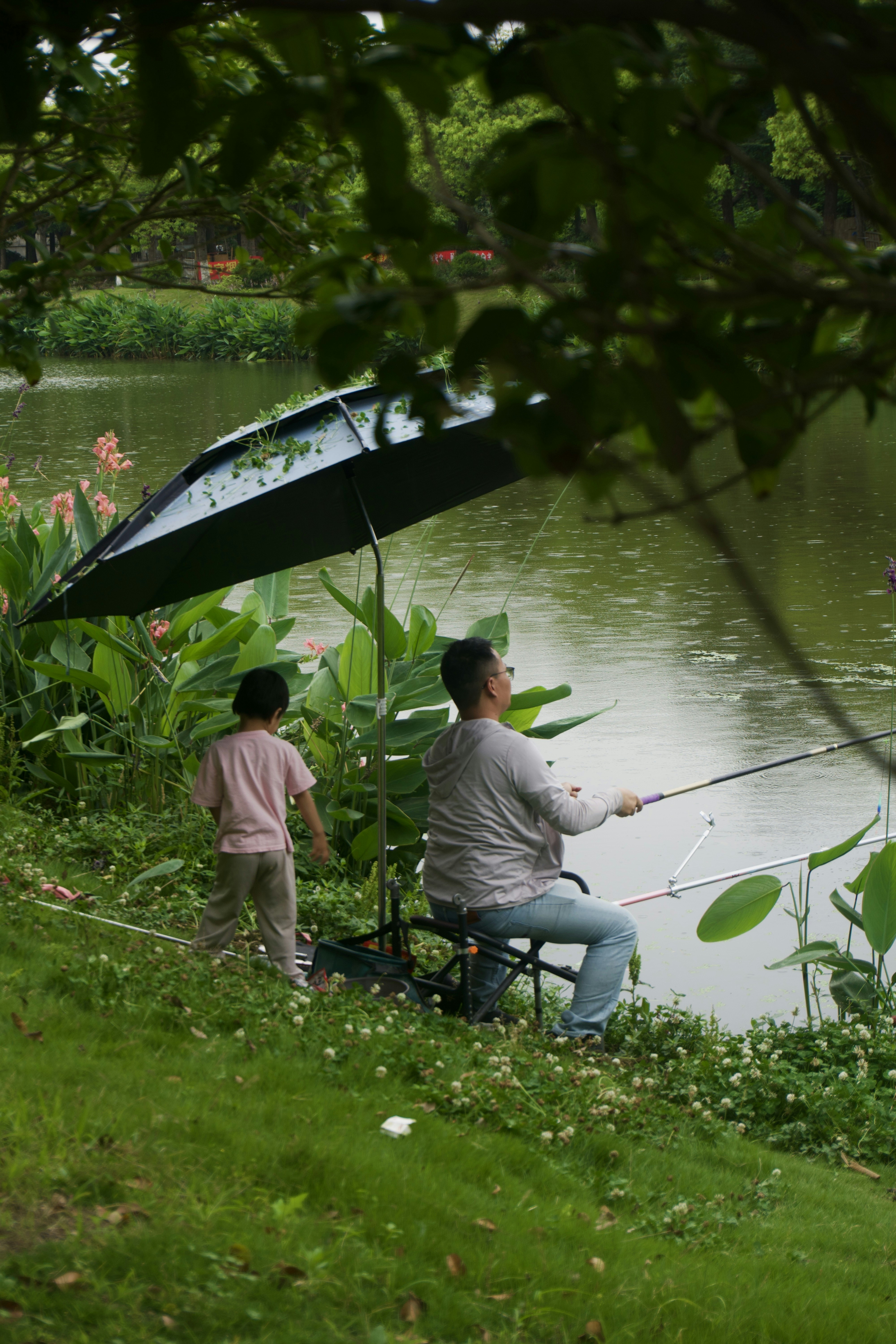 Quiet Moment by the Lake: Father and Son Fishing Under a Park Umbrella