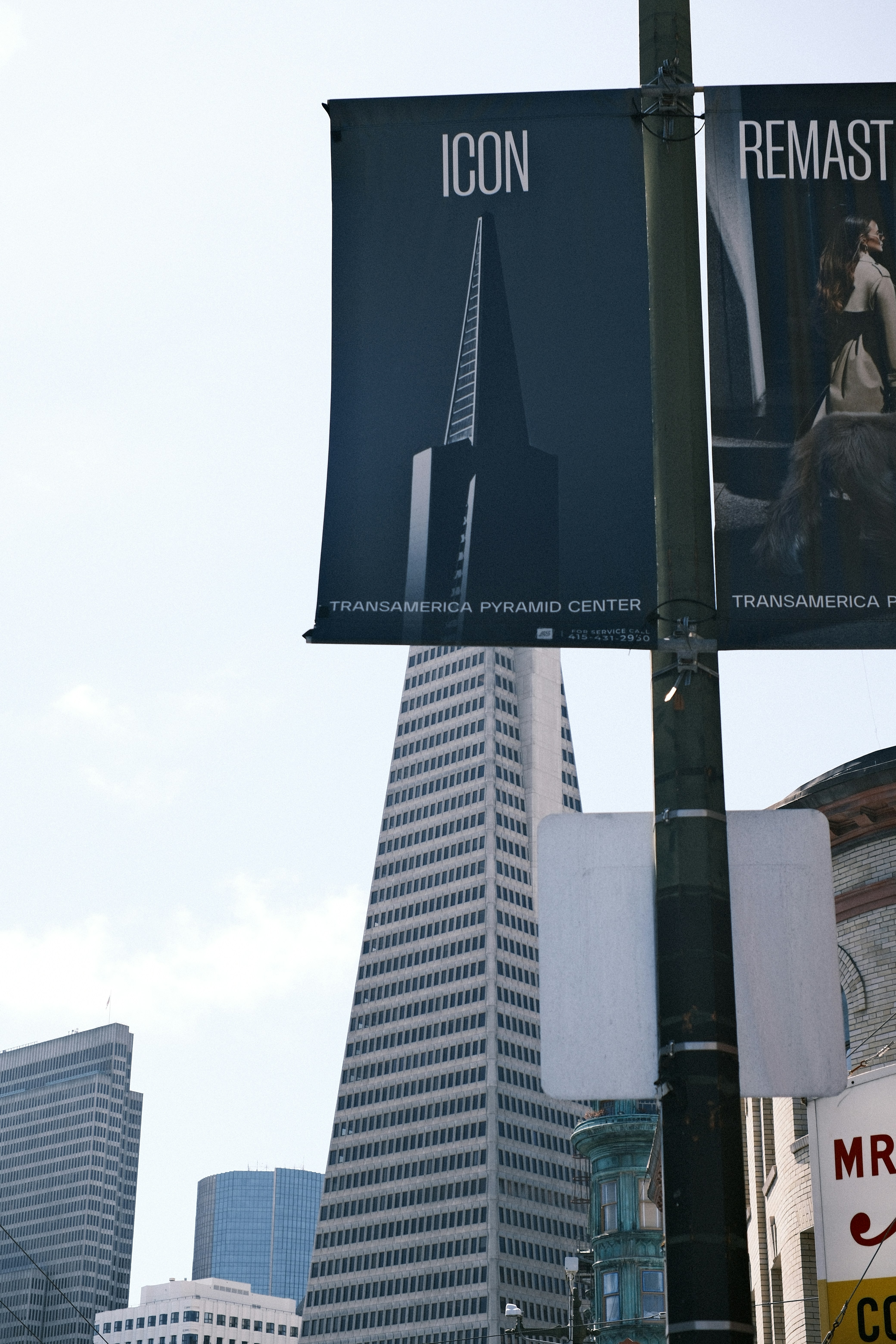 Bannered city street with a tall, pointed skyscraper peeking over a lamp post; the image highlights architectural contrast and urban signage with a clear sky backdrop.