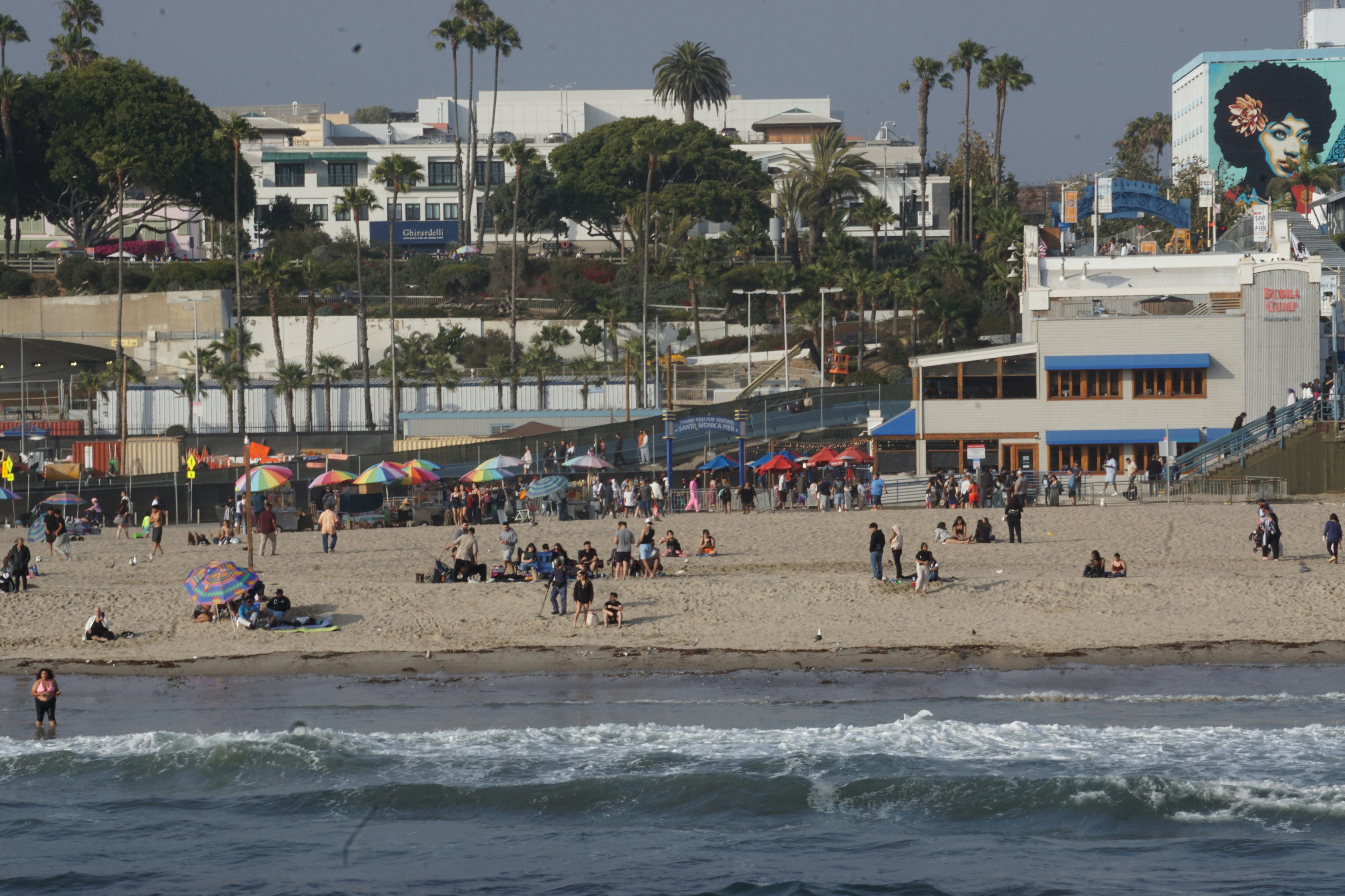 Sunlit Strand: Beachgoers and Urban Backdrop under a Pollock-like Sky
