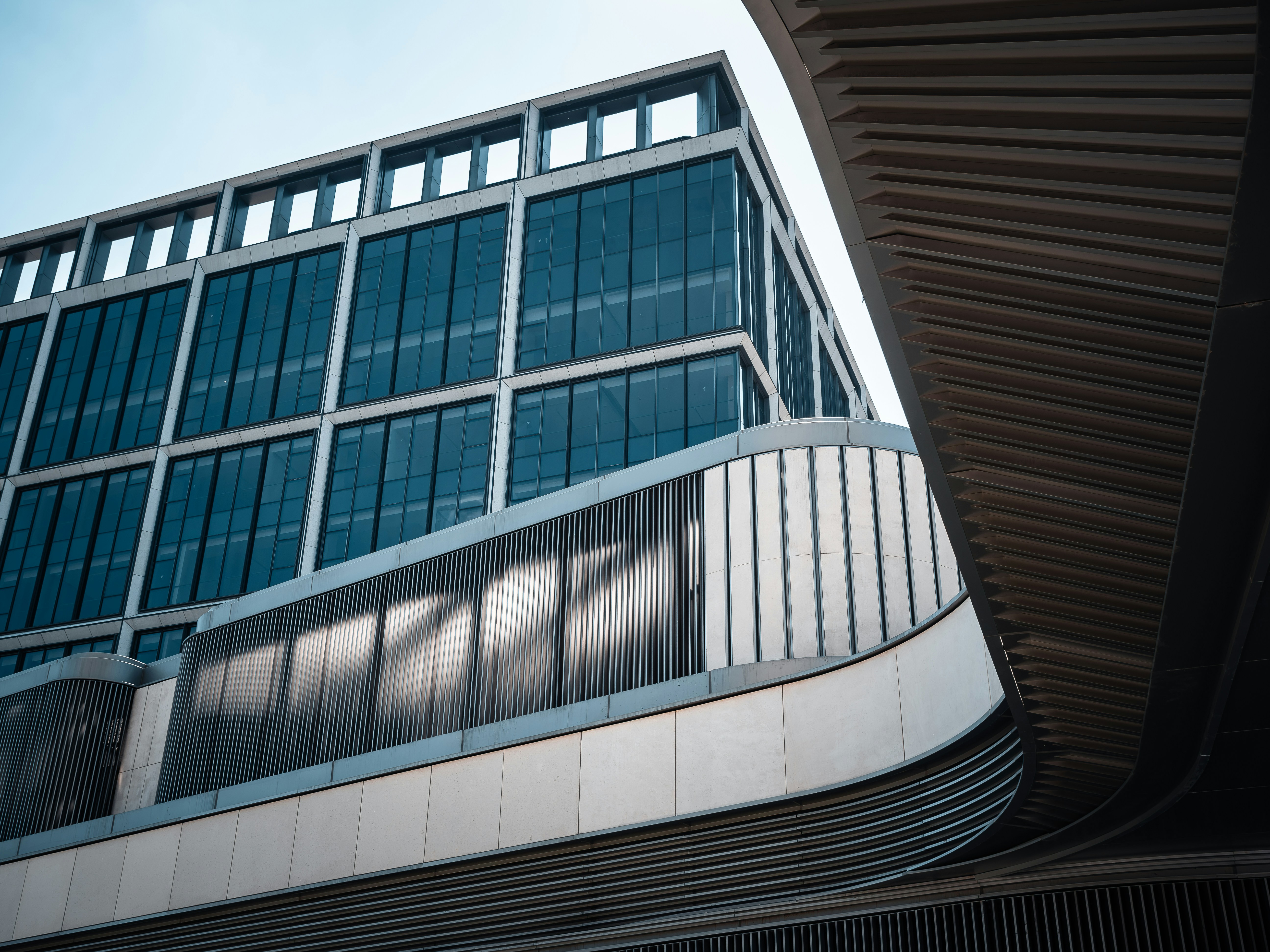 A sleek glass-and-metal building corner with layered horizontal lines and curved accents, captured in daylight to emphasize architectural form and texture.